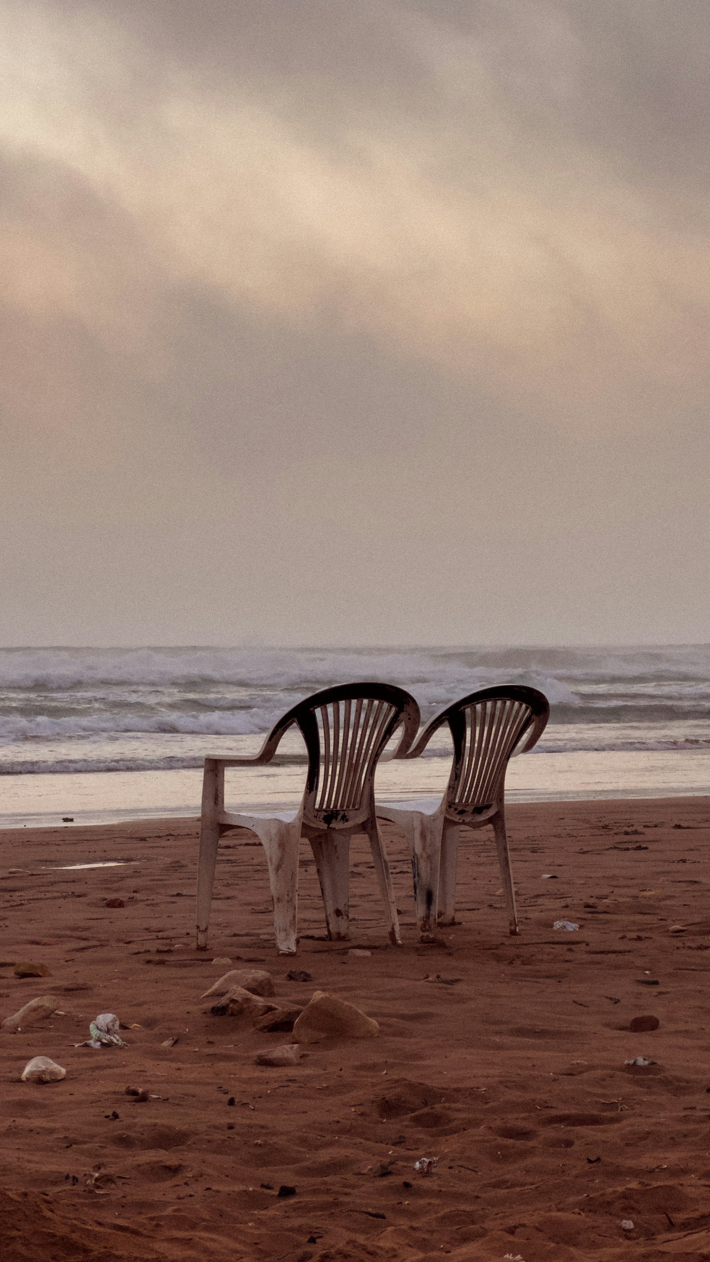 Two plastic chairs on a reddish-brown beach by the ocean.