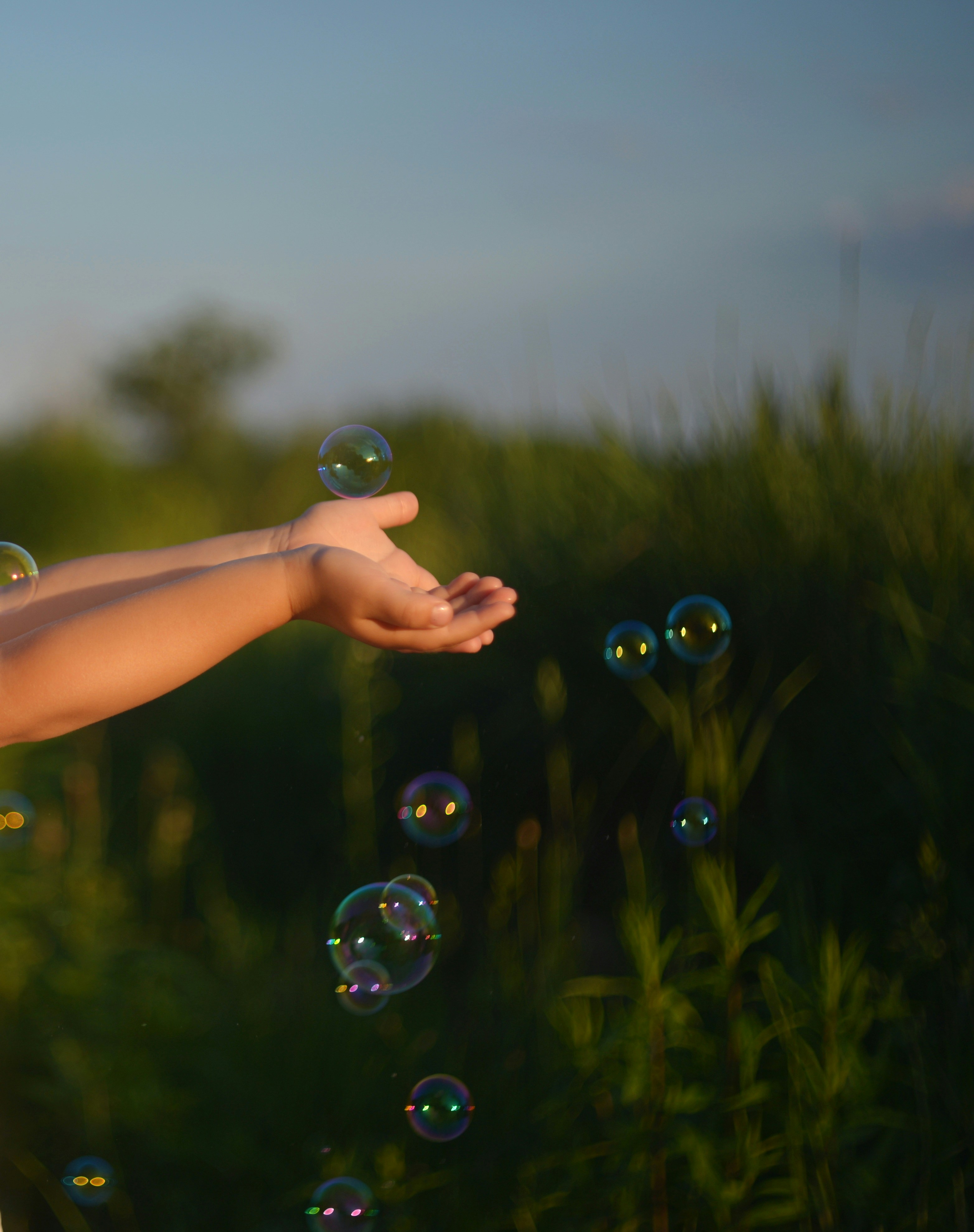 Hands releasing soap bubbles at golden hour with blurred grassy backdrop