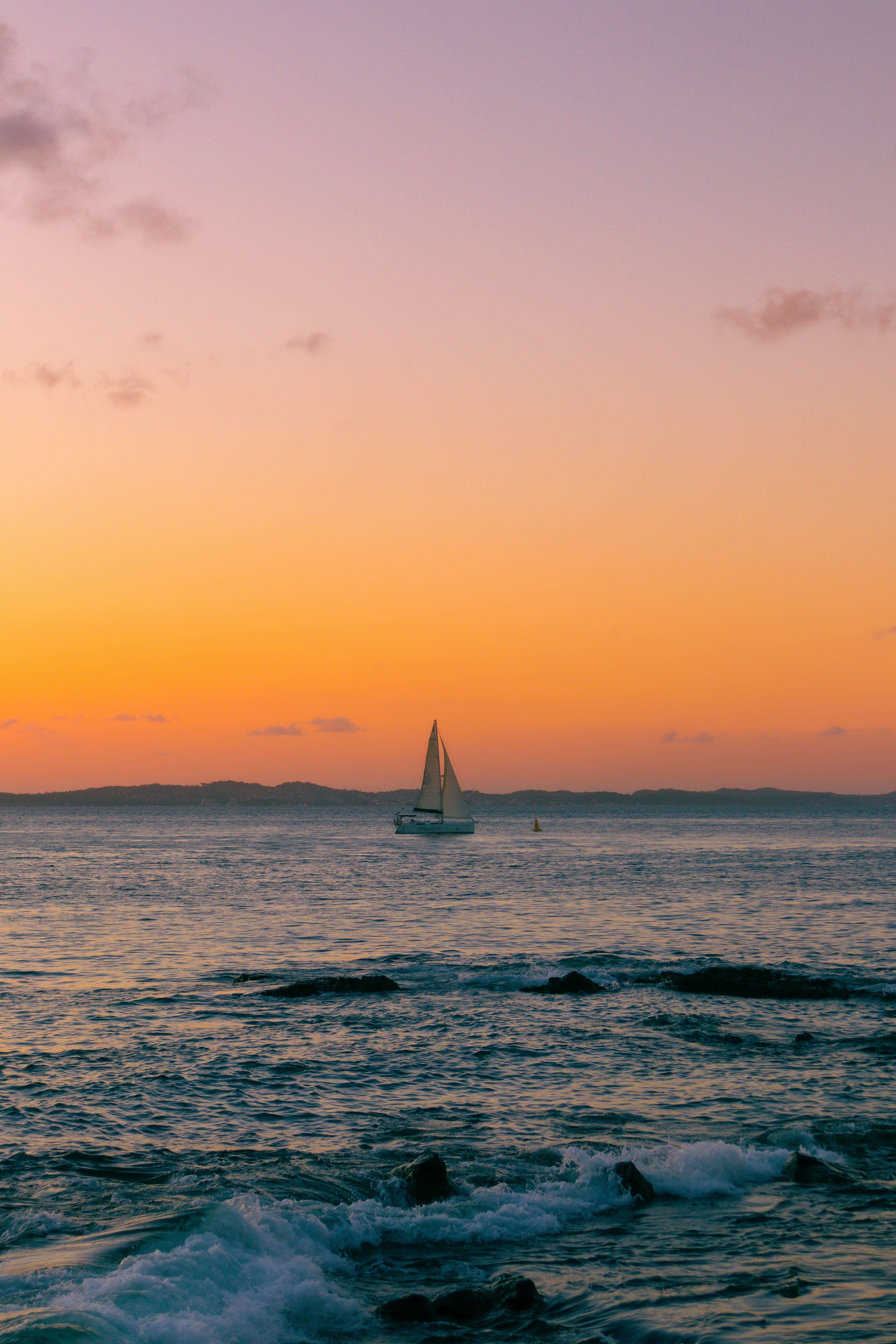 Vibrant sunset over the ocean with a distant sailboat.