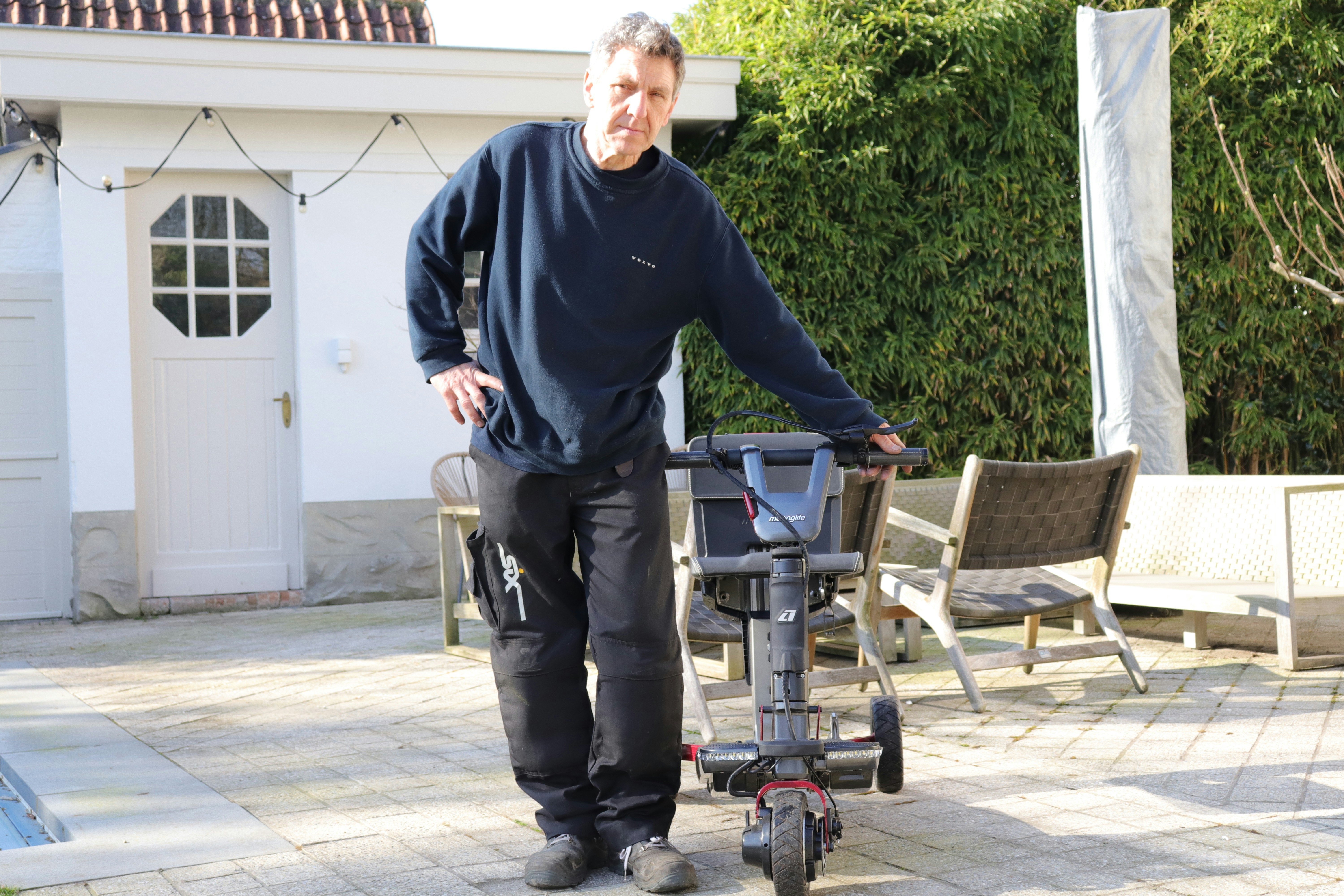 Man with an electric scooter/stair-climbing device in a sunlit backyard