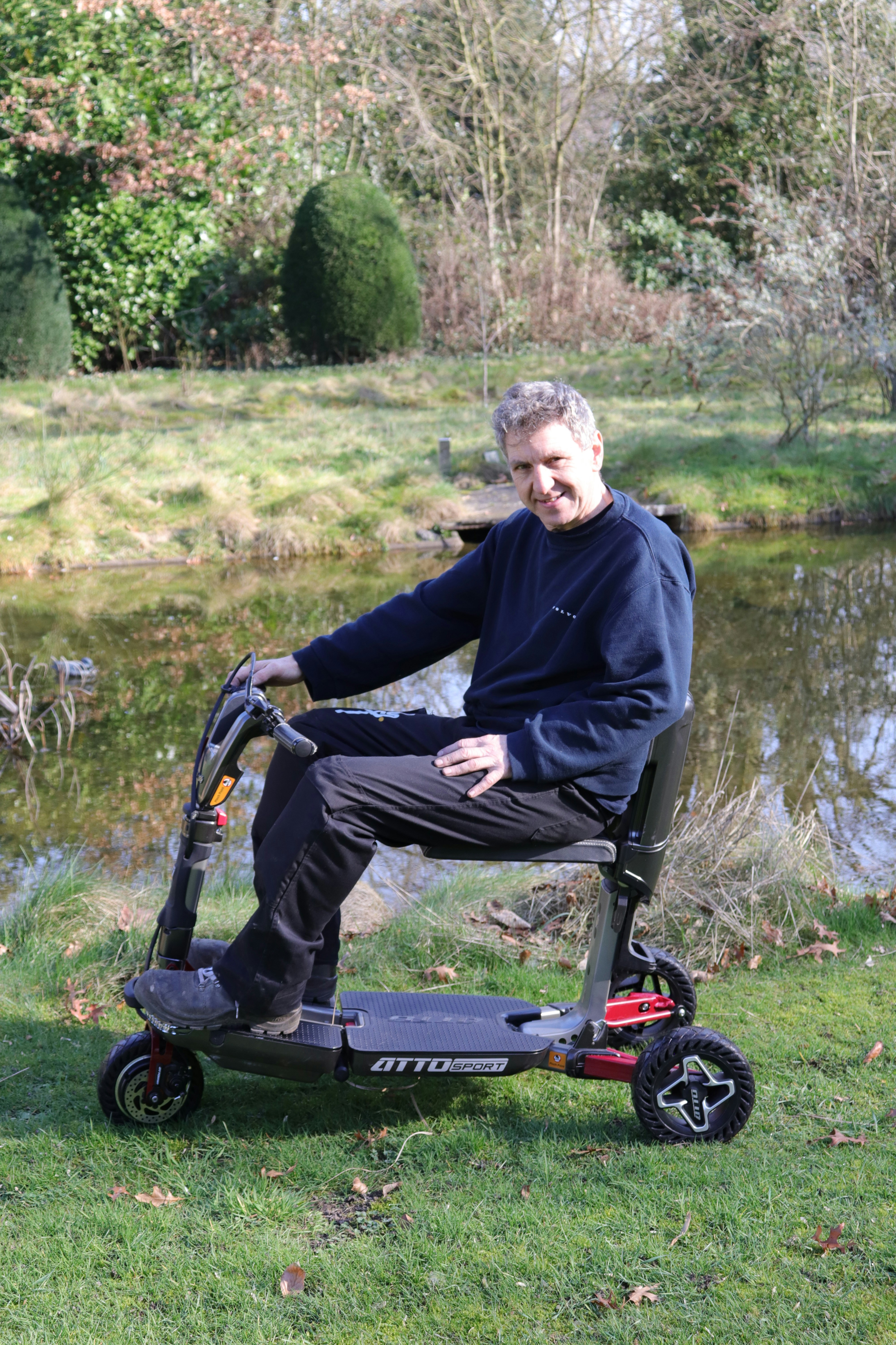 Man on a motorized scooter by a pond in a garden