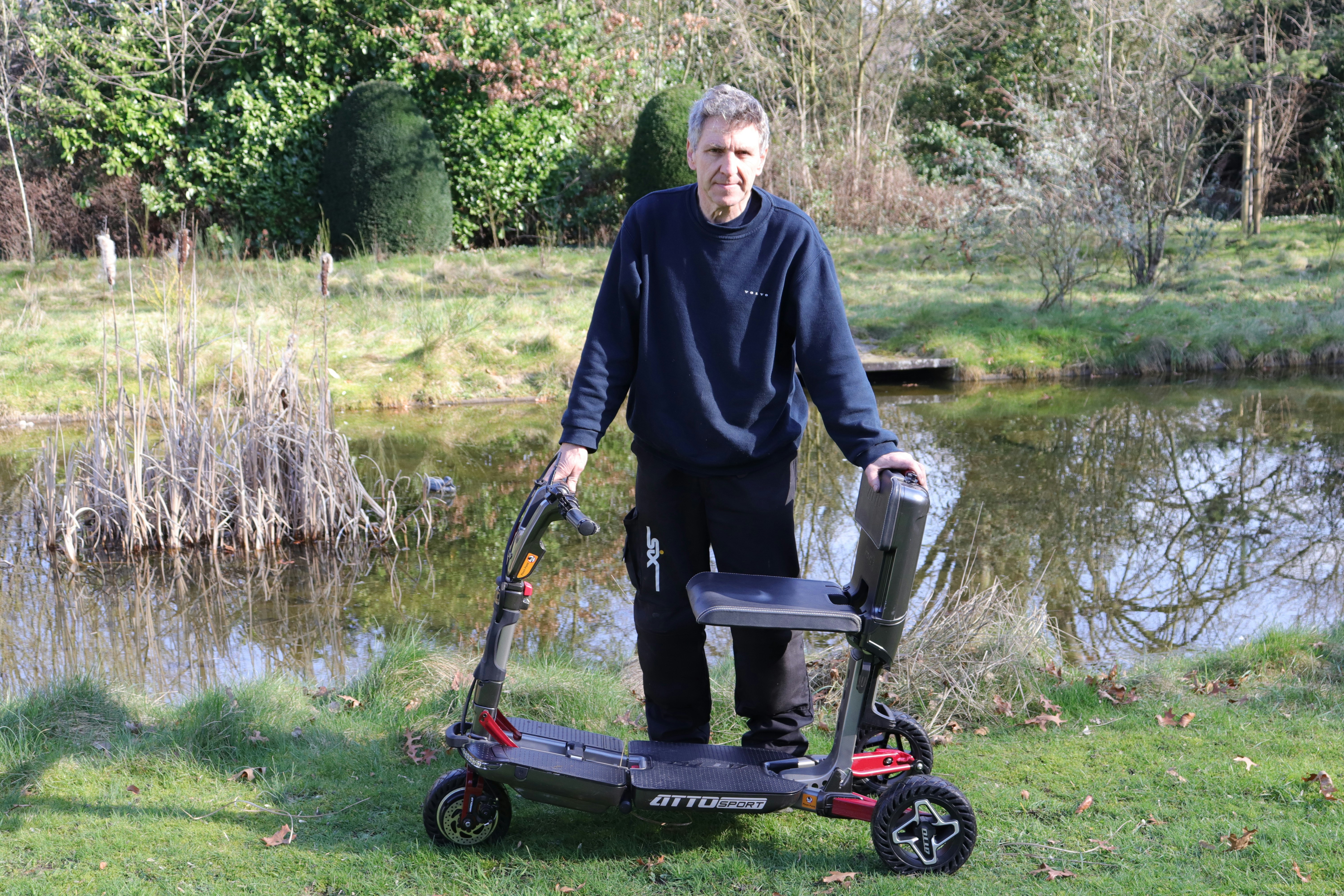 Man with electric scooter on a sunny lakeside lawn
