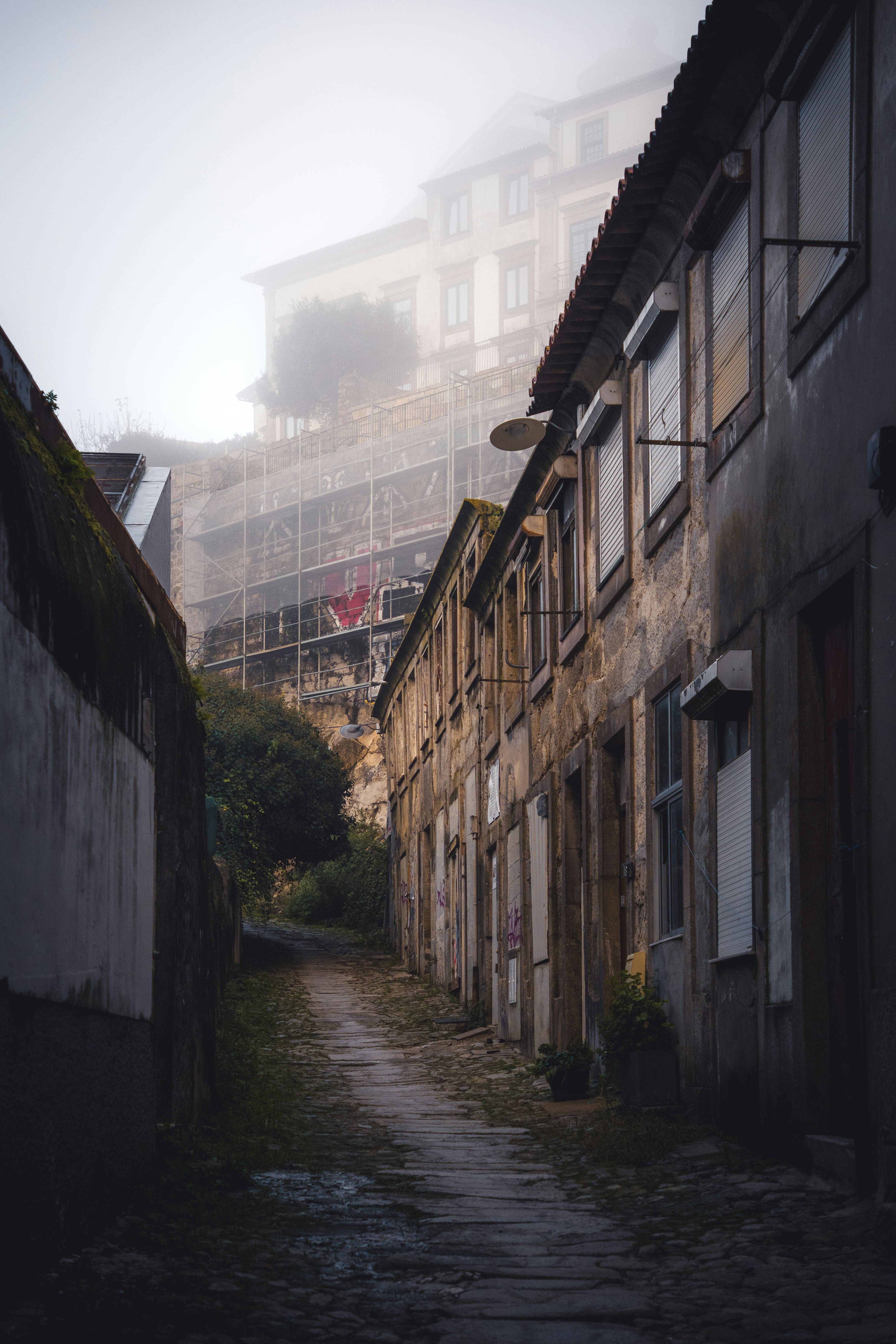 Foggy, narrow cobblestone alley with old buildings.