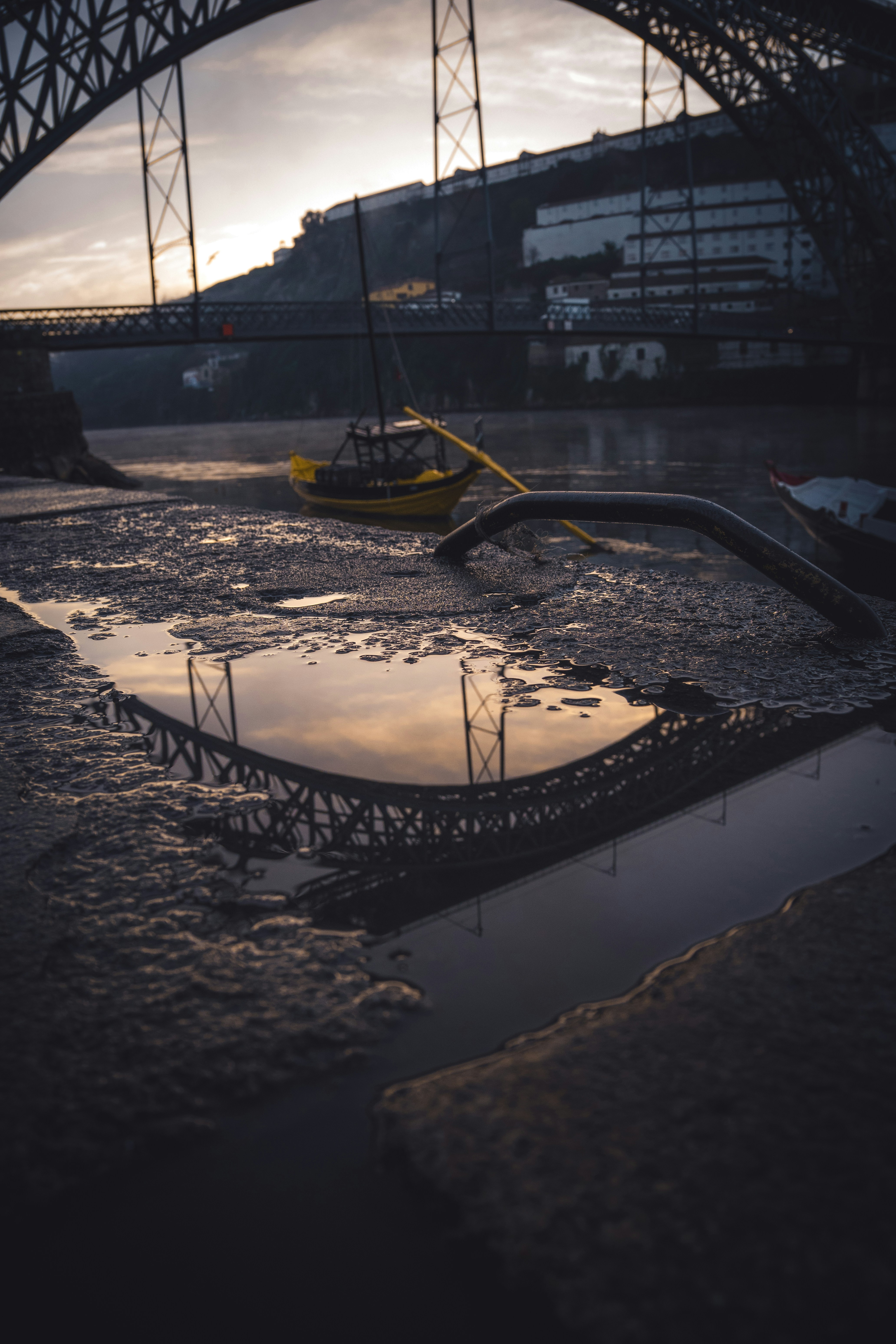 Metal bridge reflected in muddy water with a yellow boat.