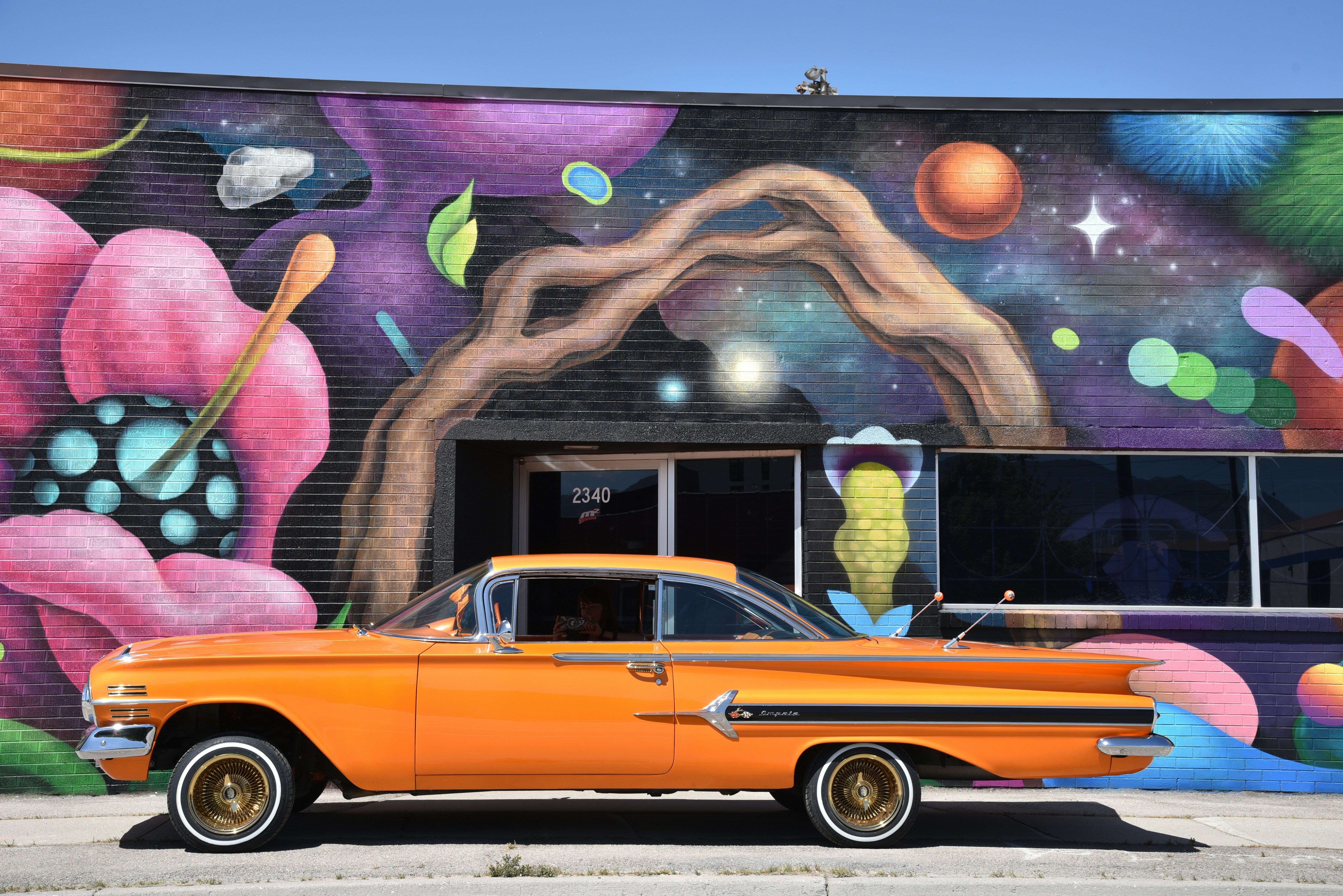 Orange Classic: A 1950s Sedan Paused before a Cosmic Mural