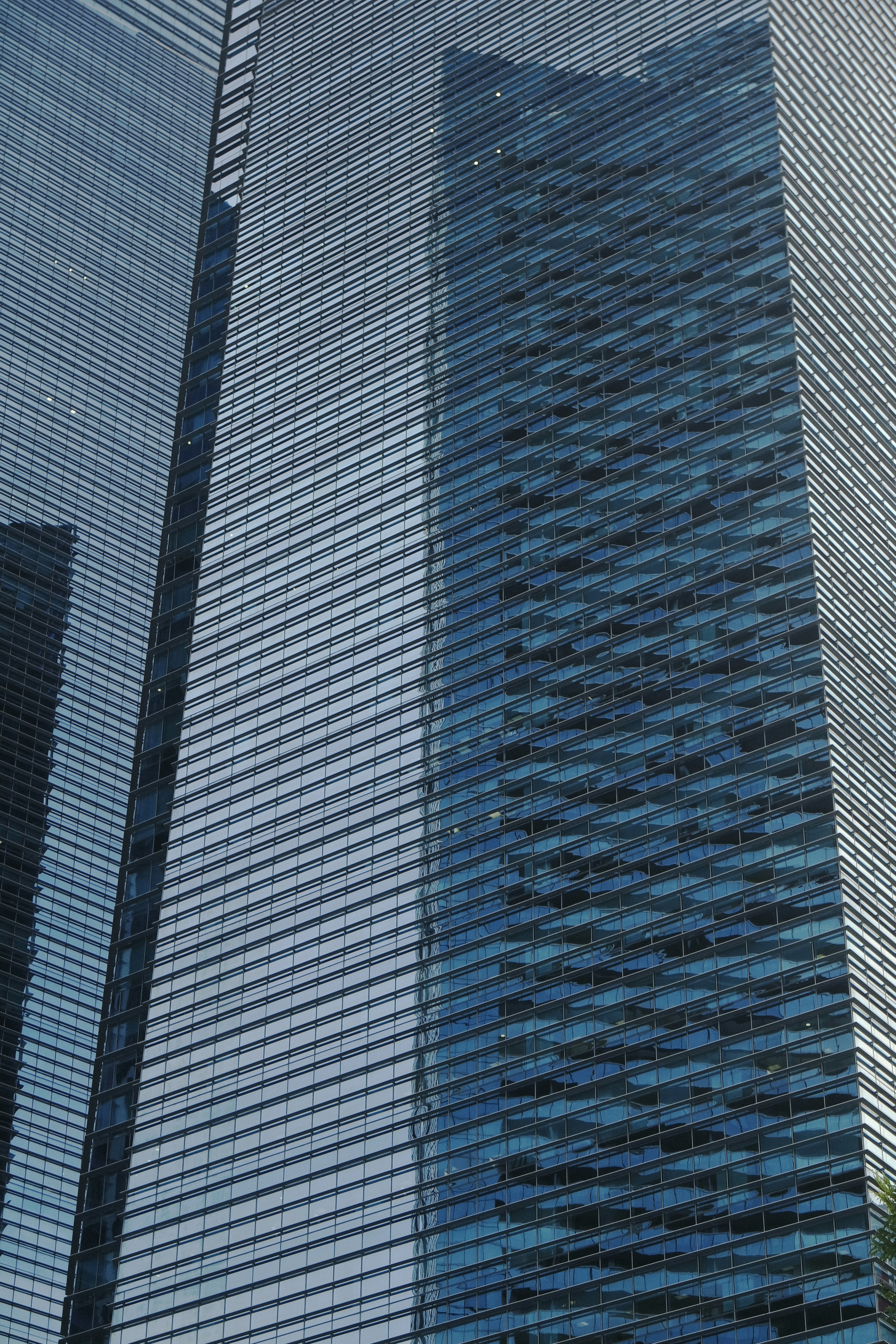 Two glass towers rise in close alignment, their facades reflecting the cityscape in cool tones. Architectural detail and repetitive grid lines convey a geometric urban scene.