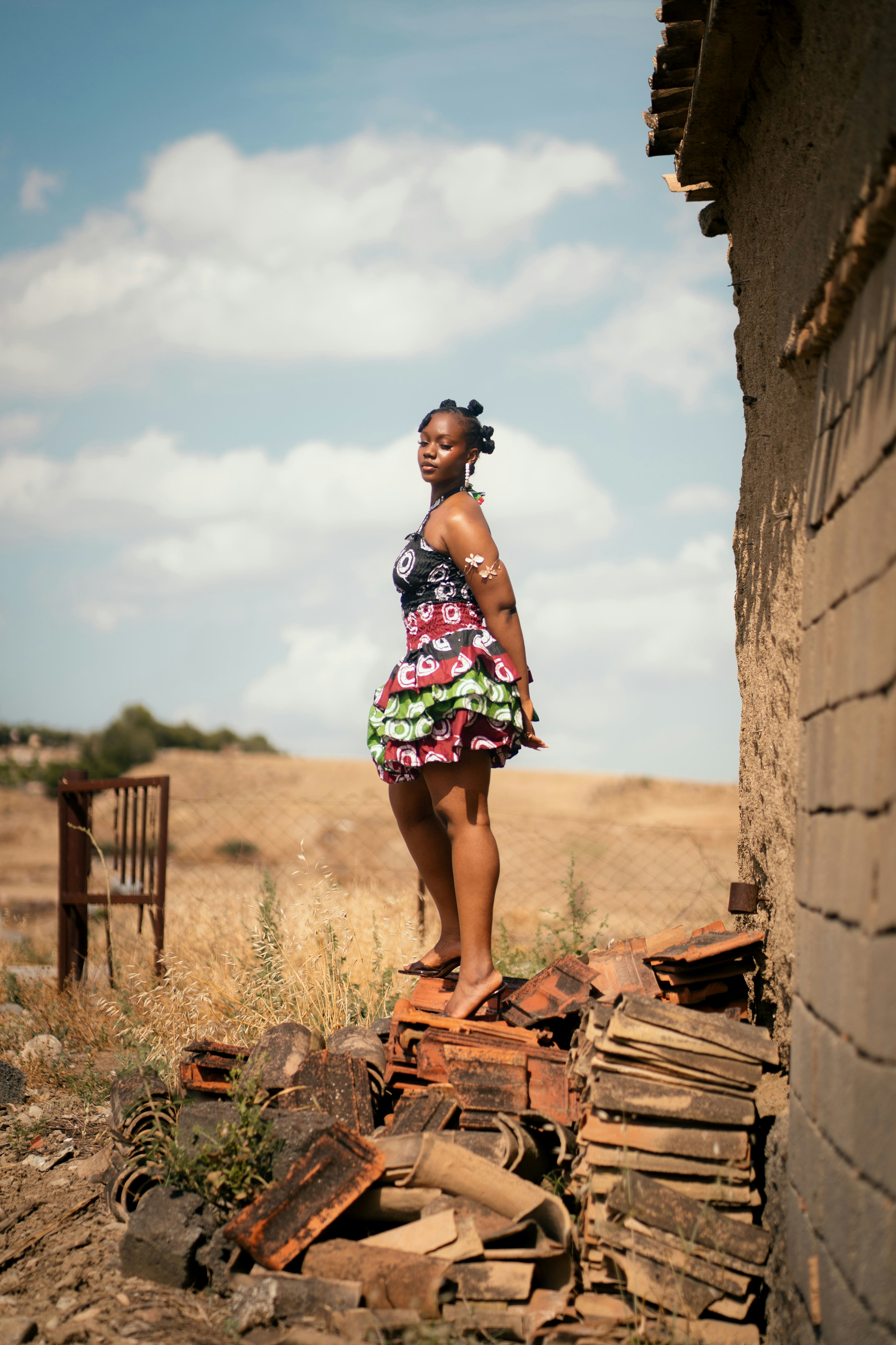 Woman Stands on Piled Tiles by a Brick Wall in Sunlit Field