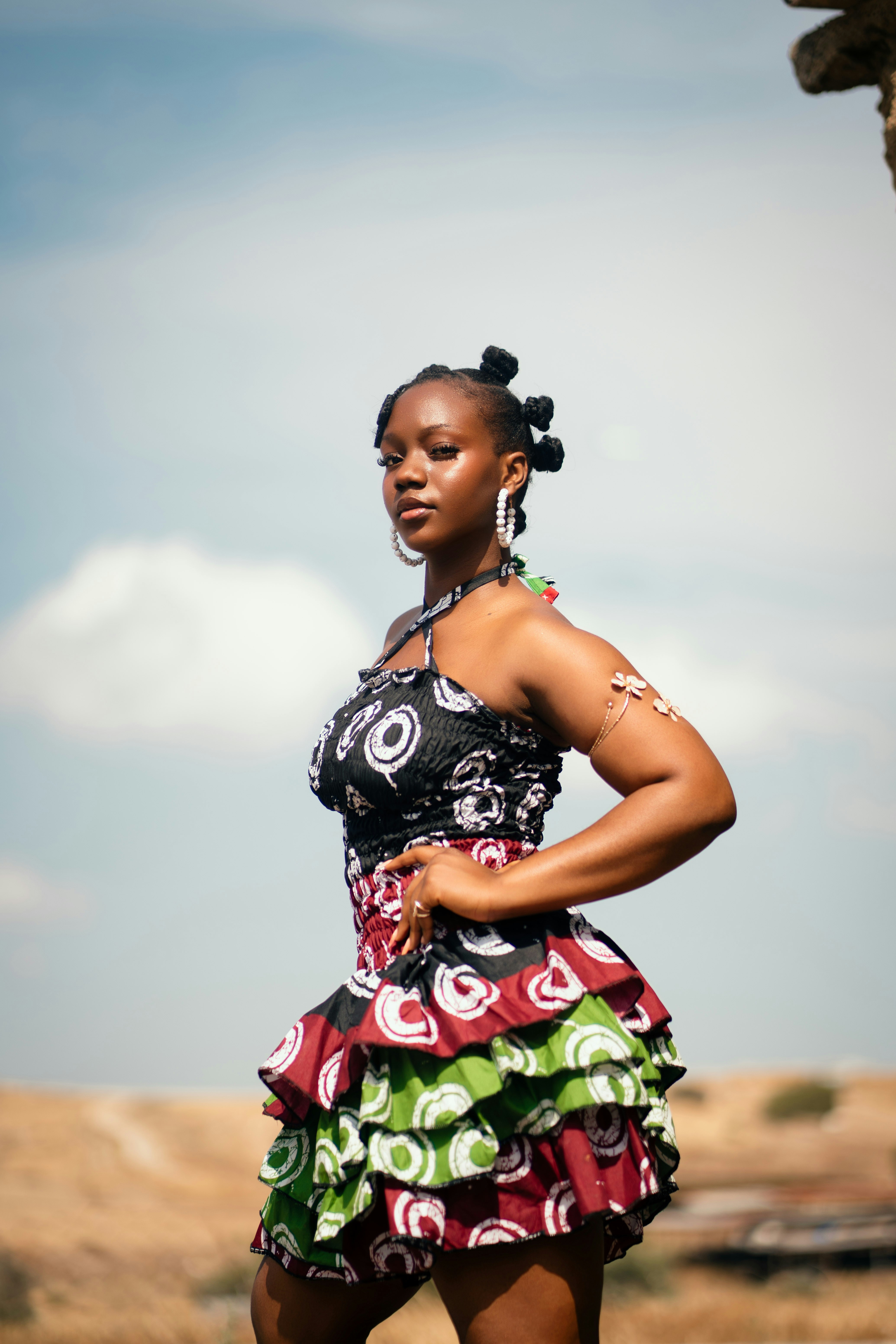 Woman in colorful patterned dress and elaborate hairstyle outdoors.