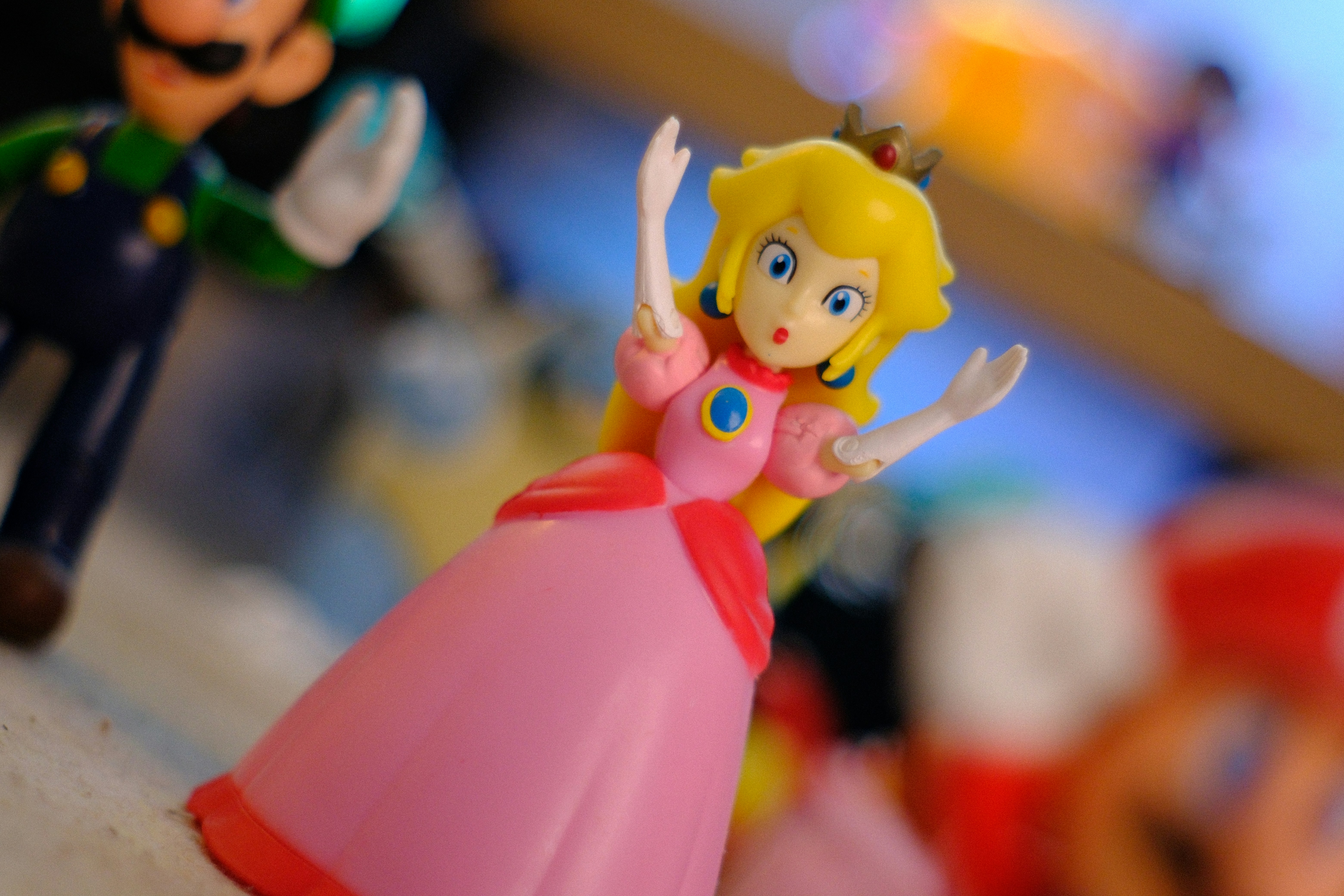 Princess peach figurine with raised arms and luigi in background.