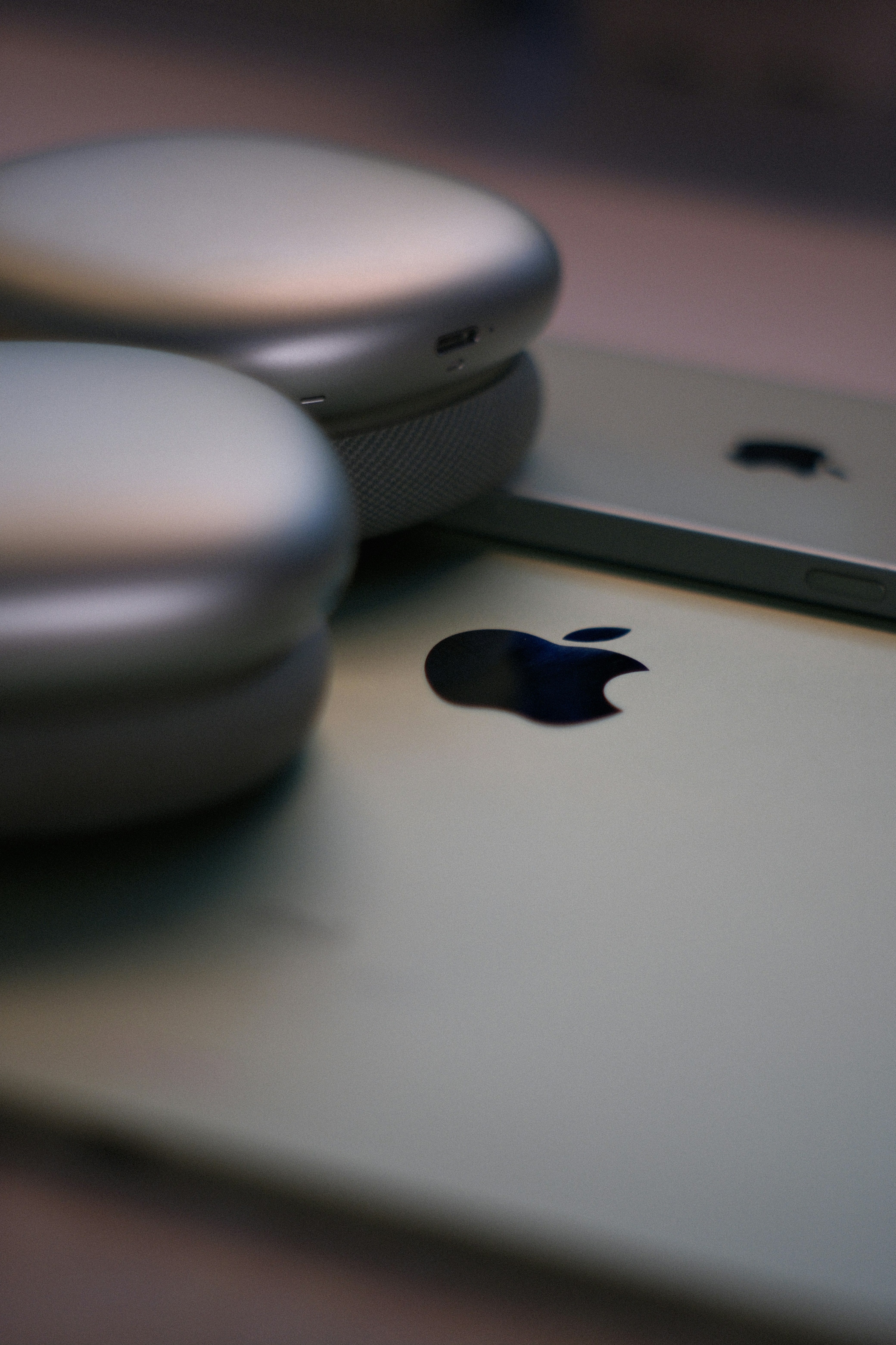 Two wireless earbuds rest atop a silver iPhone, with the iconic Apple logo visible beneath; shallow depth of field emphasizes the devices. This is a product/motif photograph of consumer electronics.