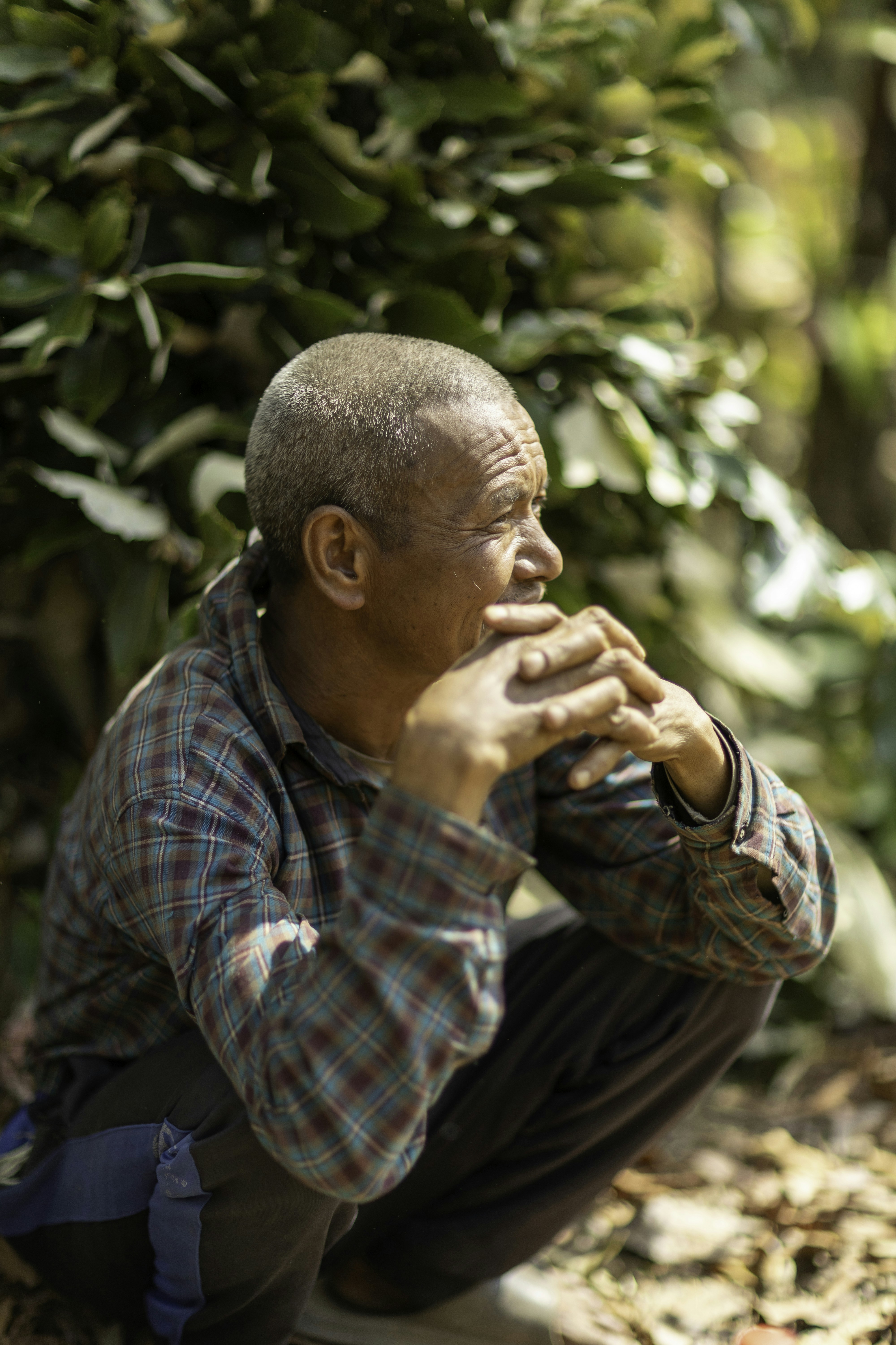 Pensive pause: a man kneels in shade, hands clasped in quiet reflection