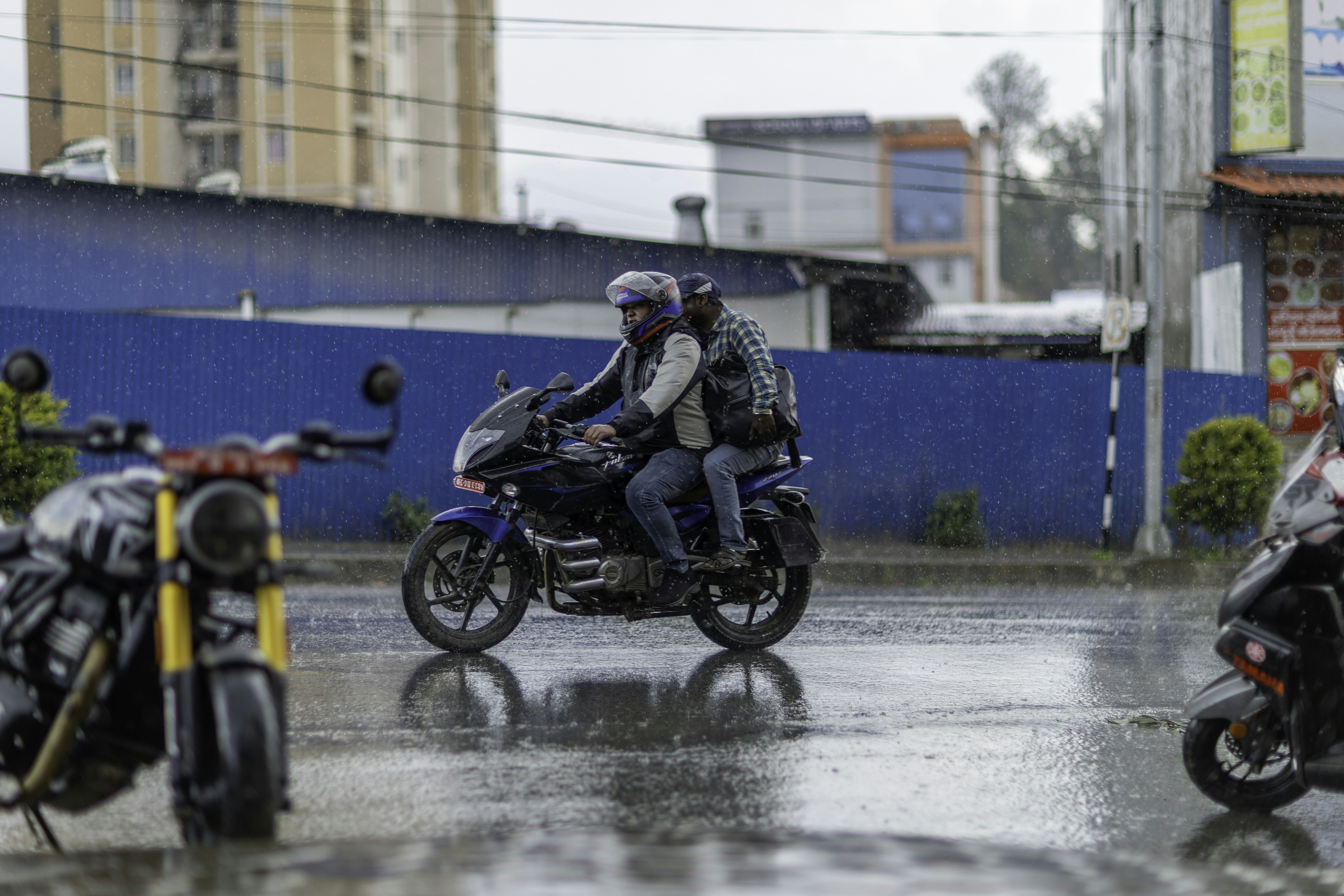 Rain-Cashed Ride: A Duo on a Blue Motorcycle Through a Wet Street