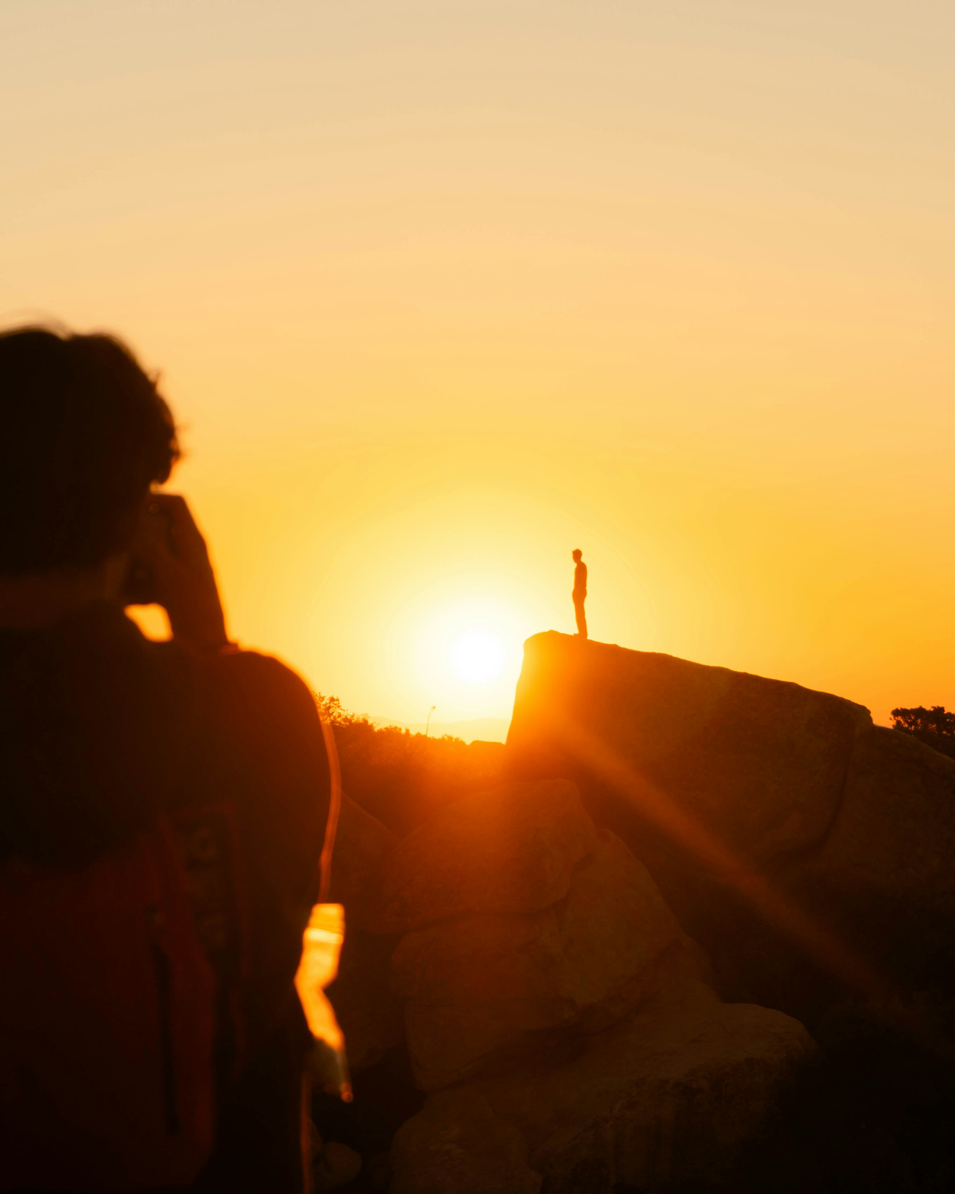 Sunlit silhouette: a lone figure on the edge of a rock at dusk