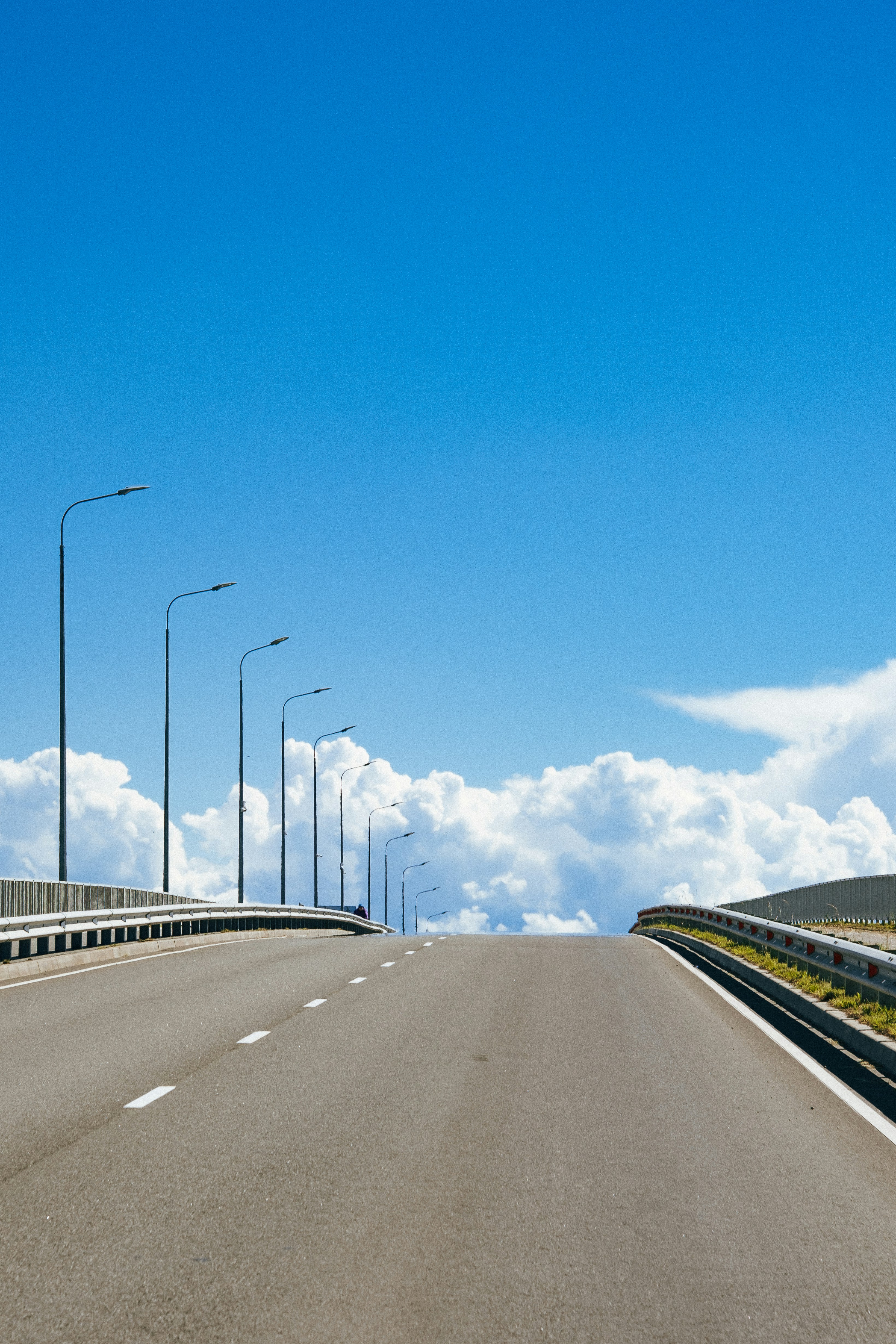 Highway ascends into a bright blue sky with fluffy clouds.