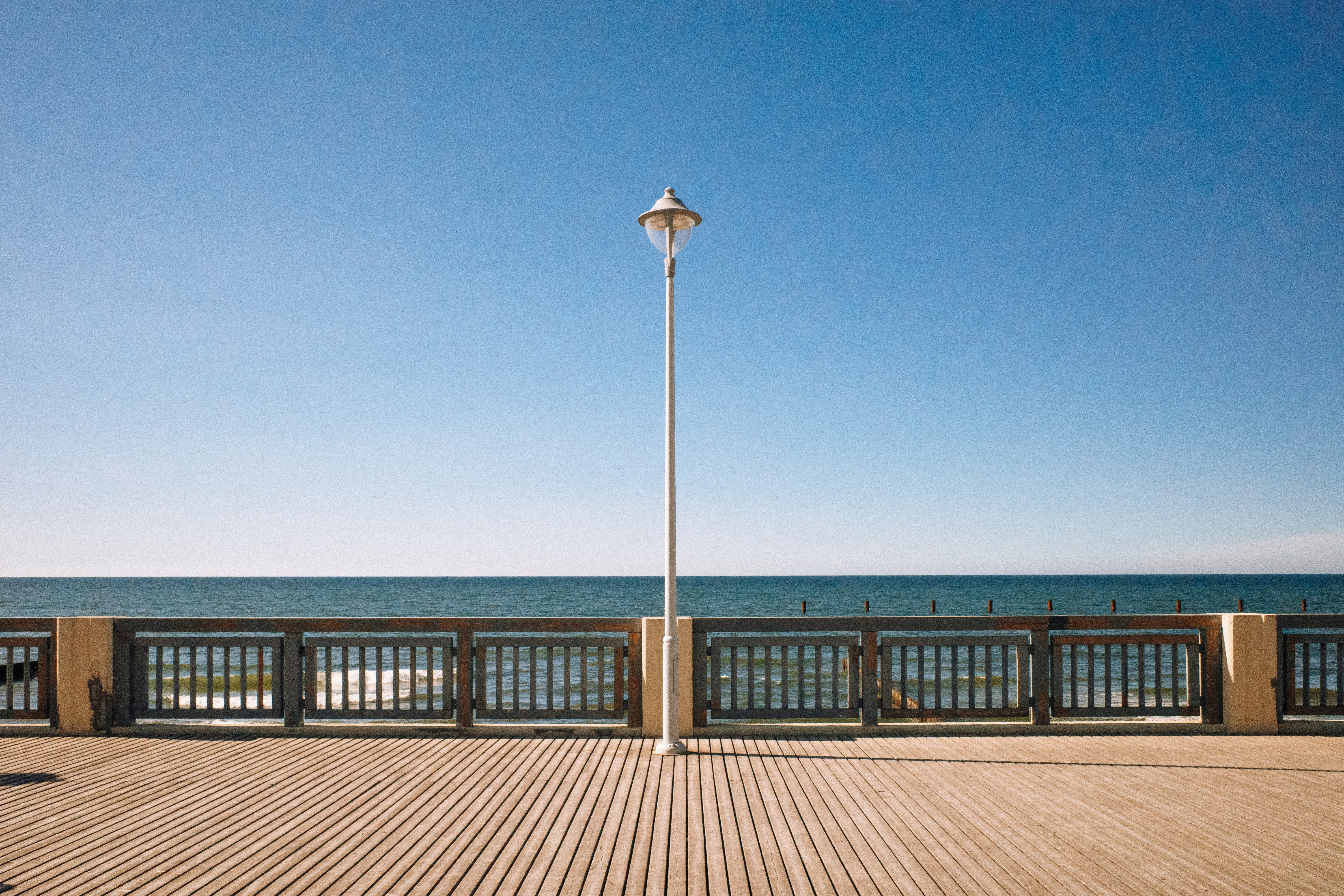A white lamppost on a wooden pier by the ocean.