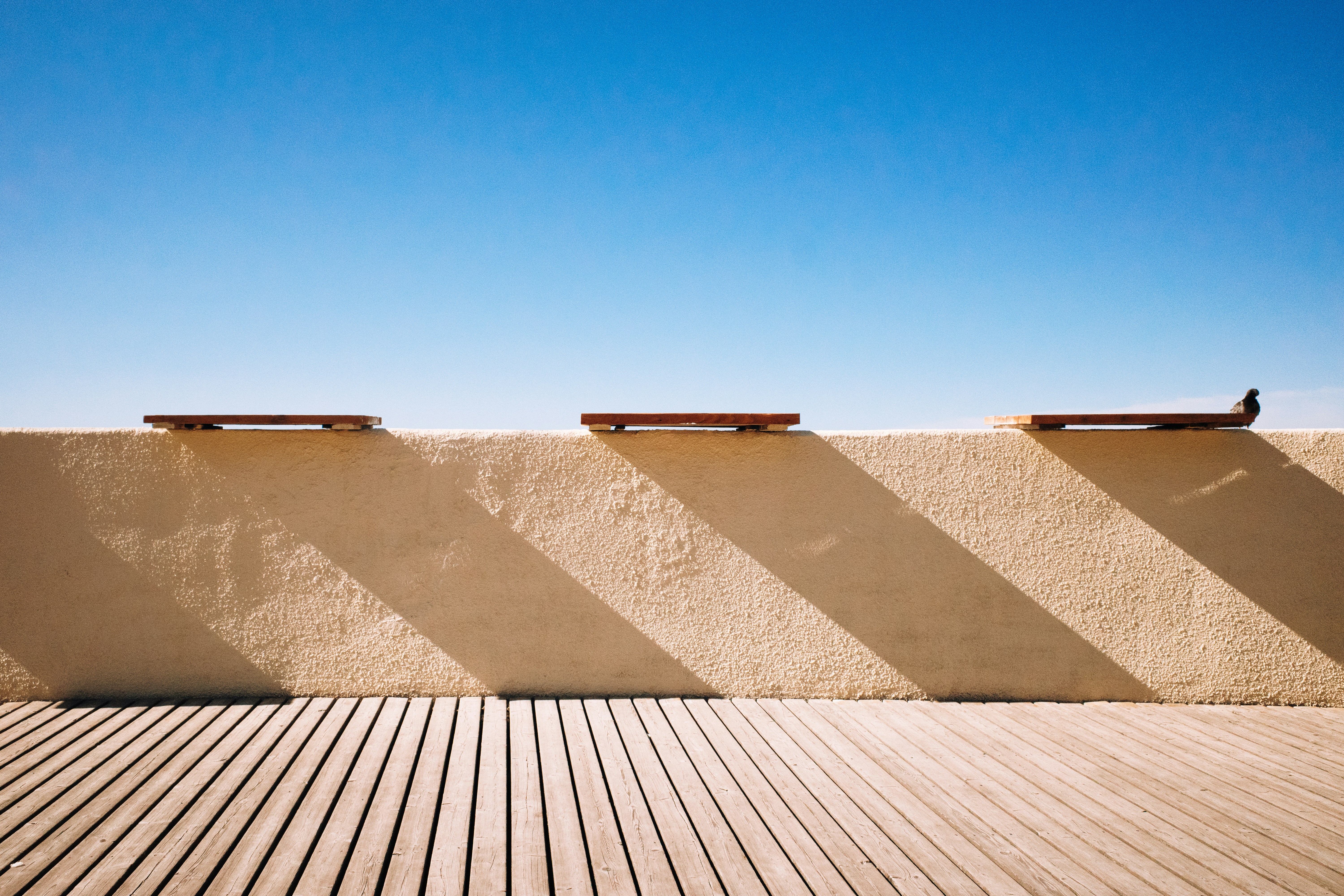 Three wooden benches on a wall with diagonal shadows.