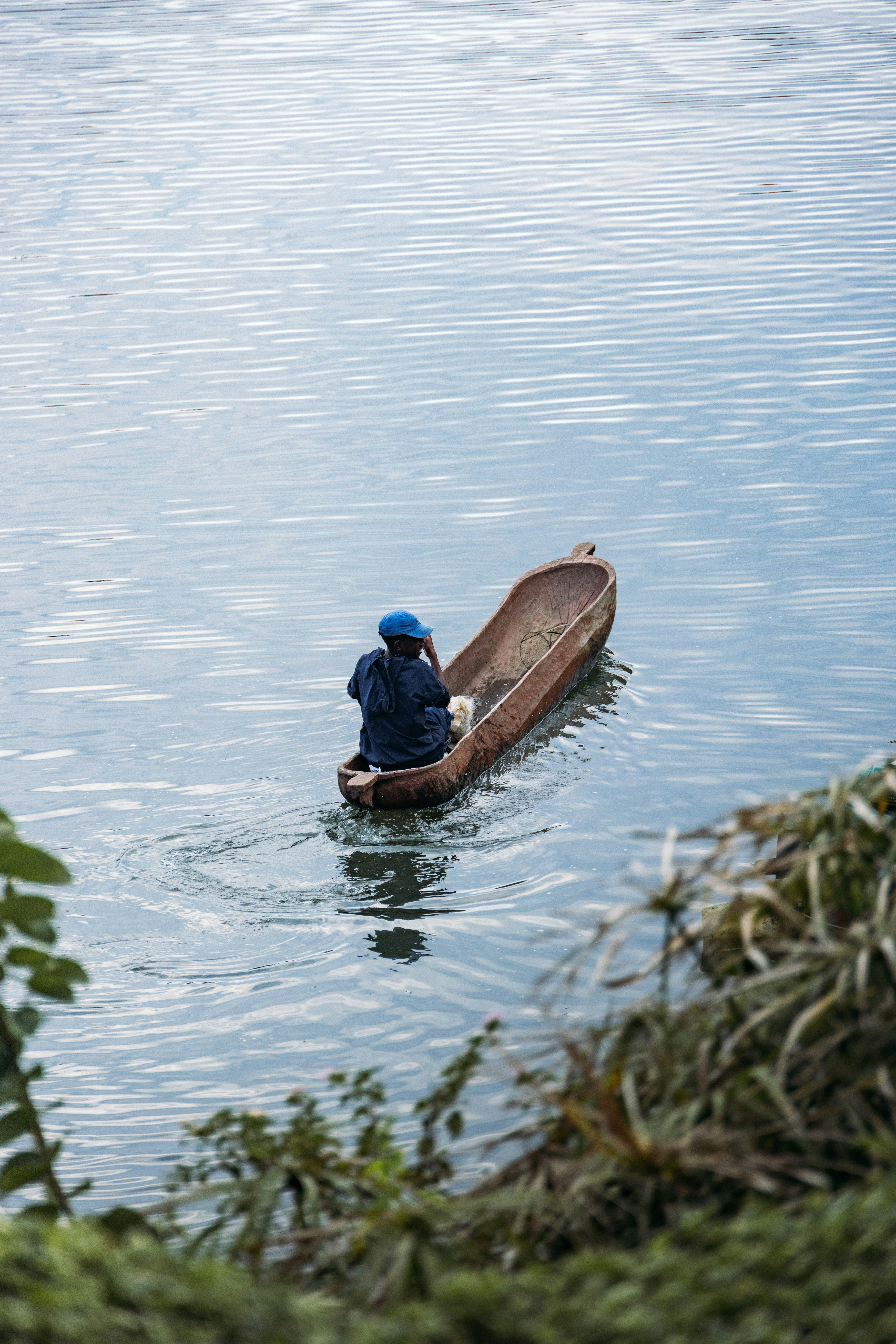 A lone paddler drifts along calm blue waters in a weathered canoe
