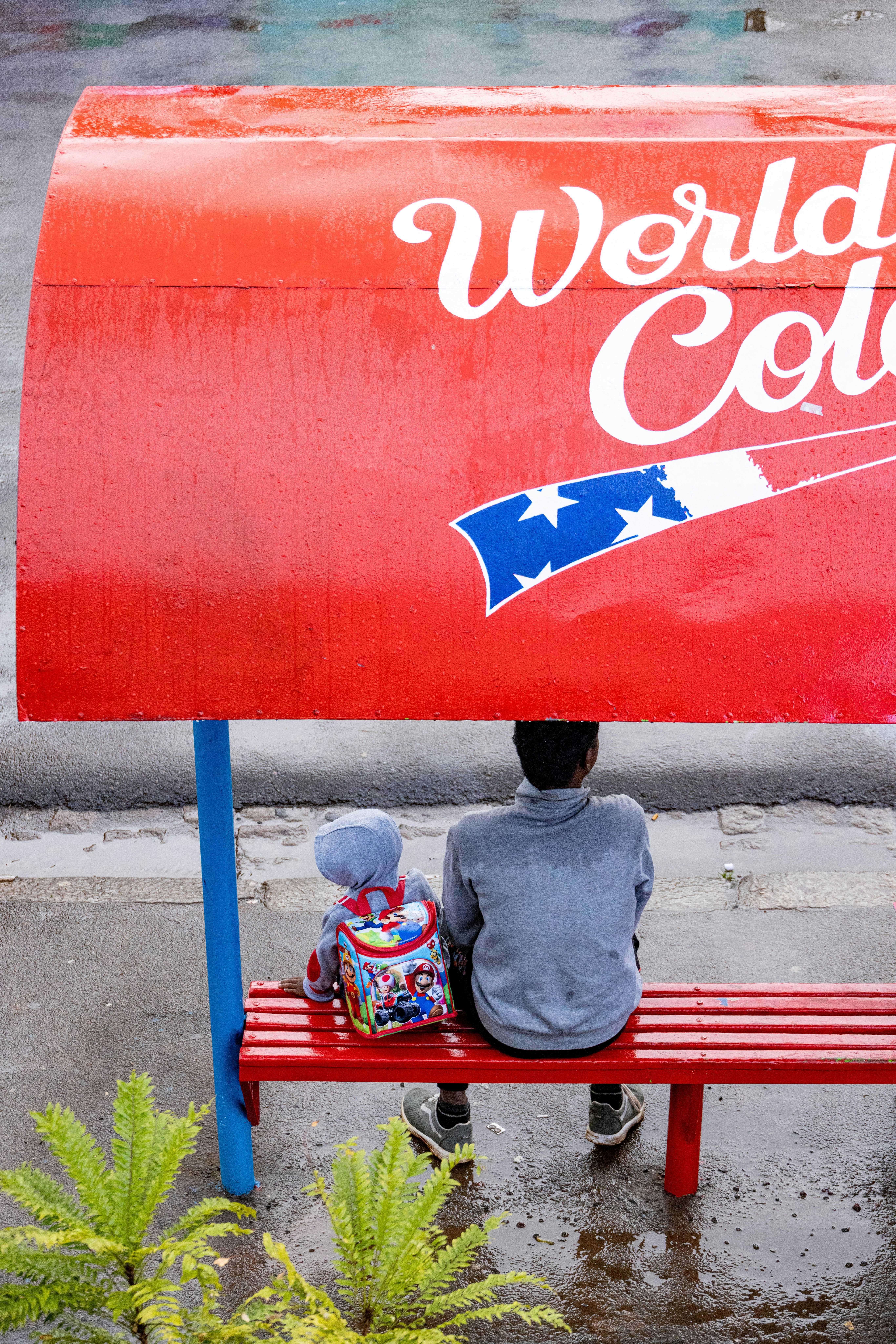 Two riders on a red bench under a vibrant advertising panel