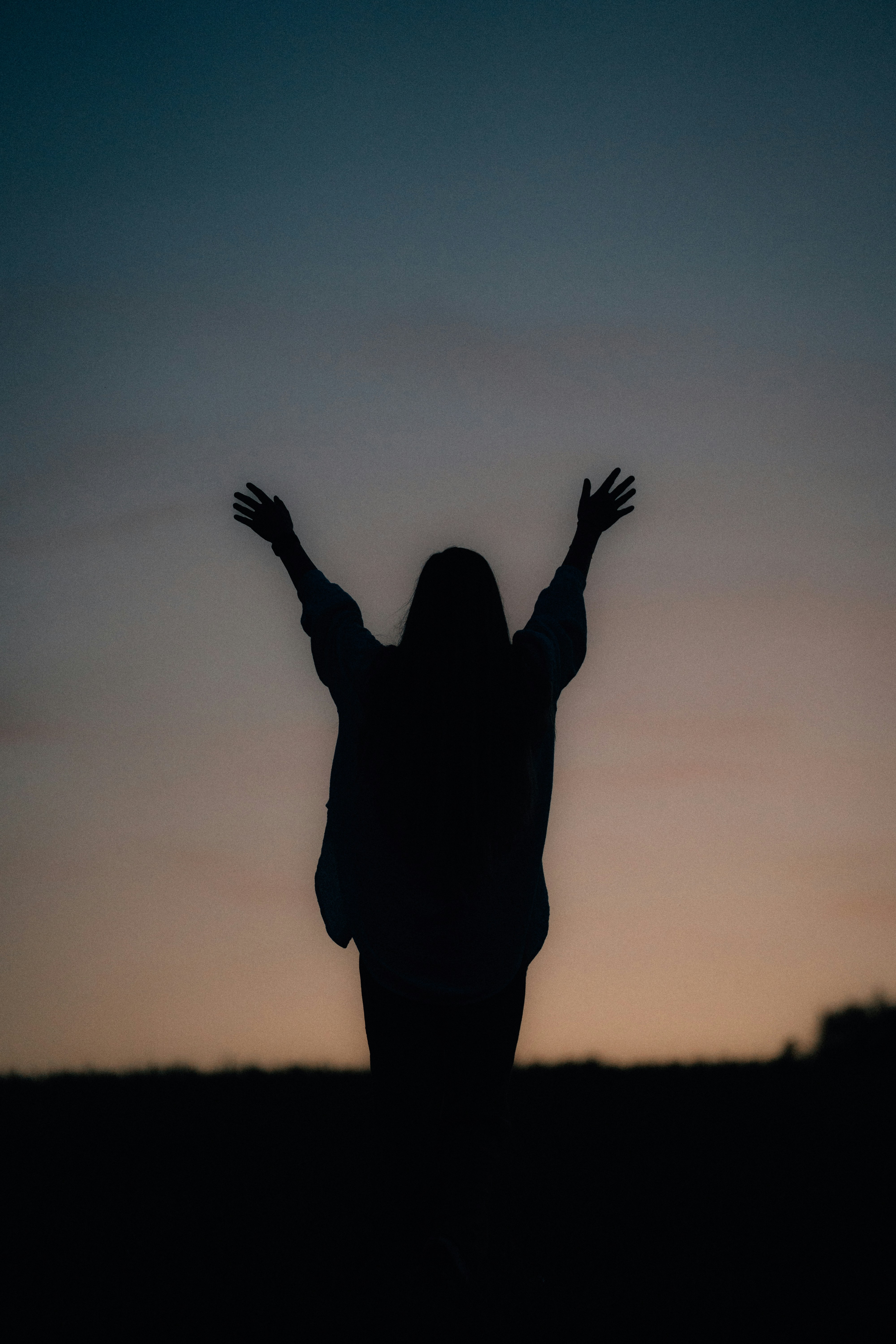 Silhouette of a person with arms raised at twilight.