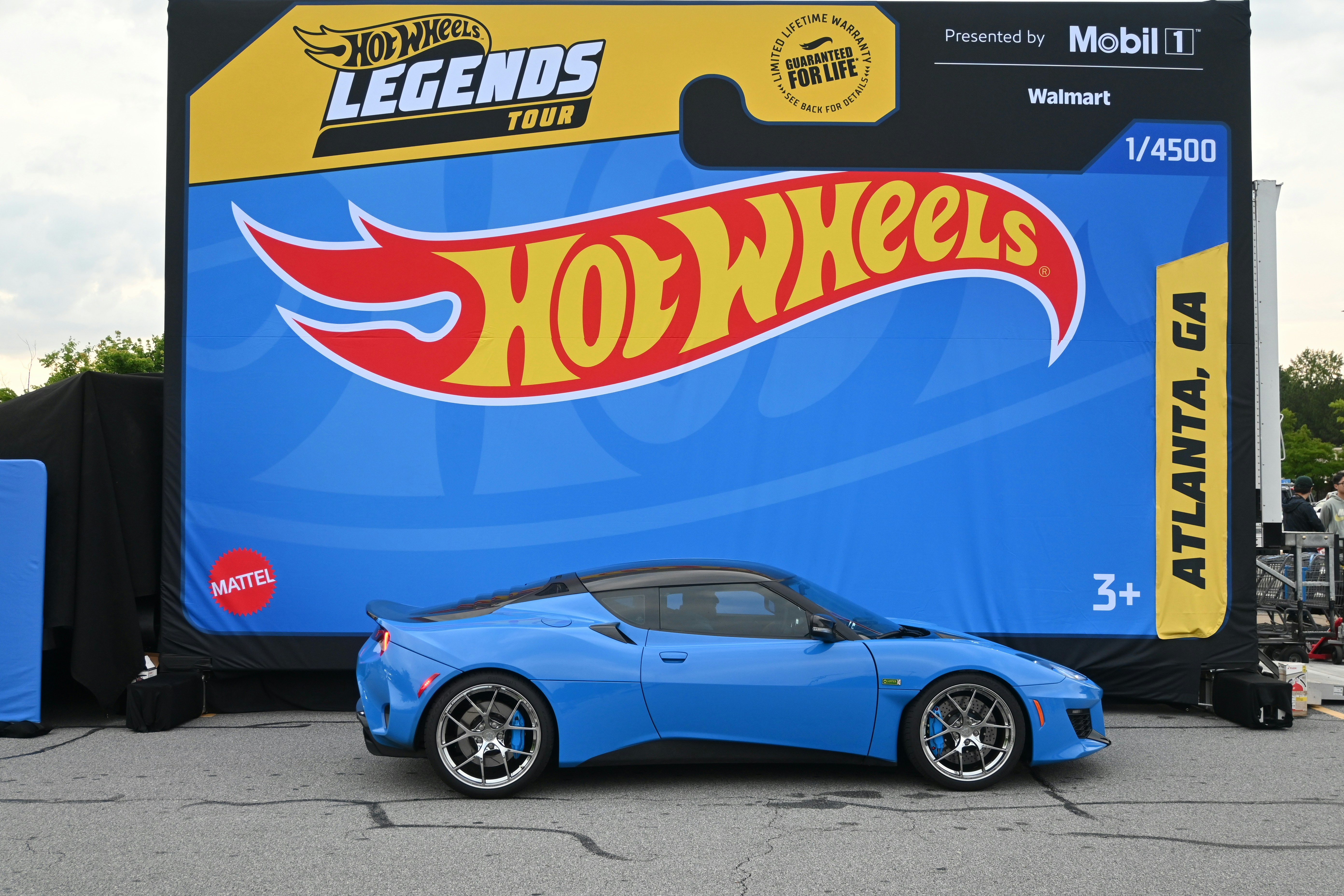 Blue sports car parked in front of a large Hot Wheels Legends Tour backdrop