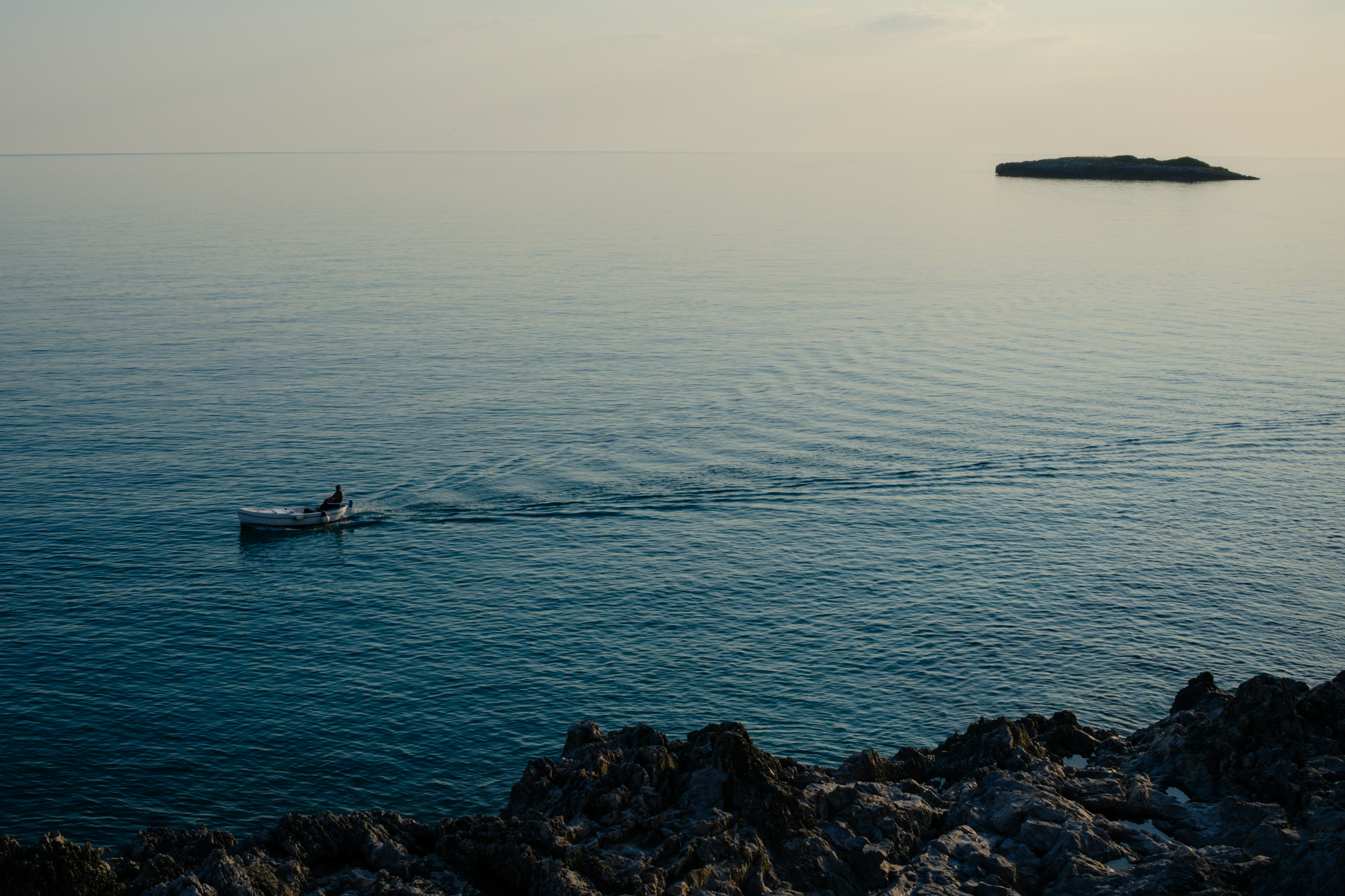 A small boat navigates calm waters towards a distant island.