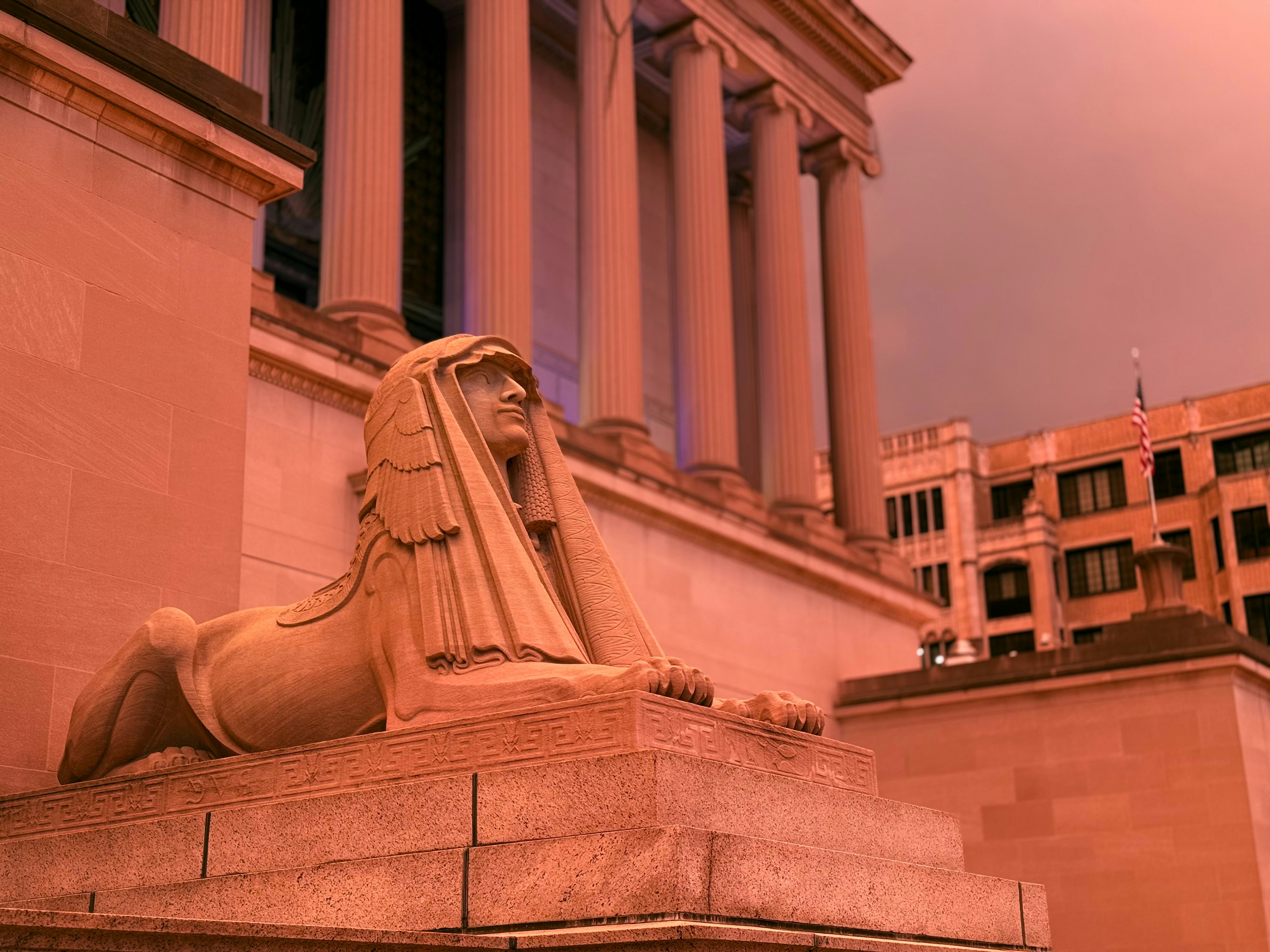 Stone sphinx statue guarding a classical building at dusk.