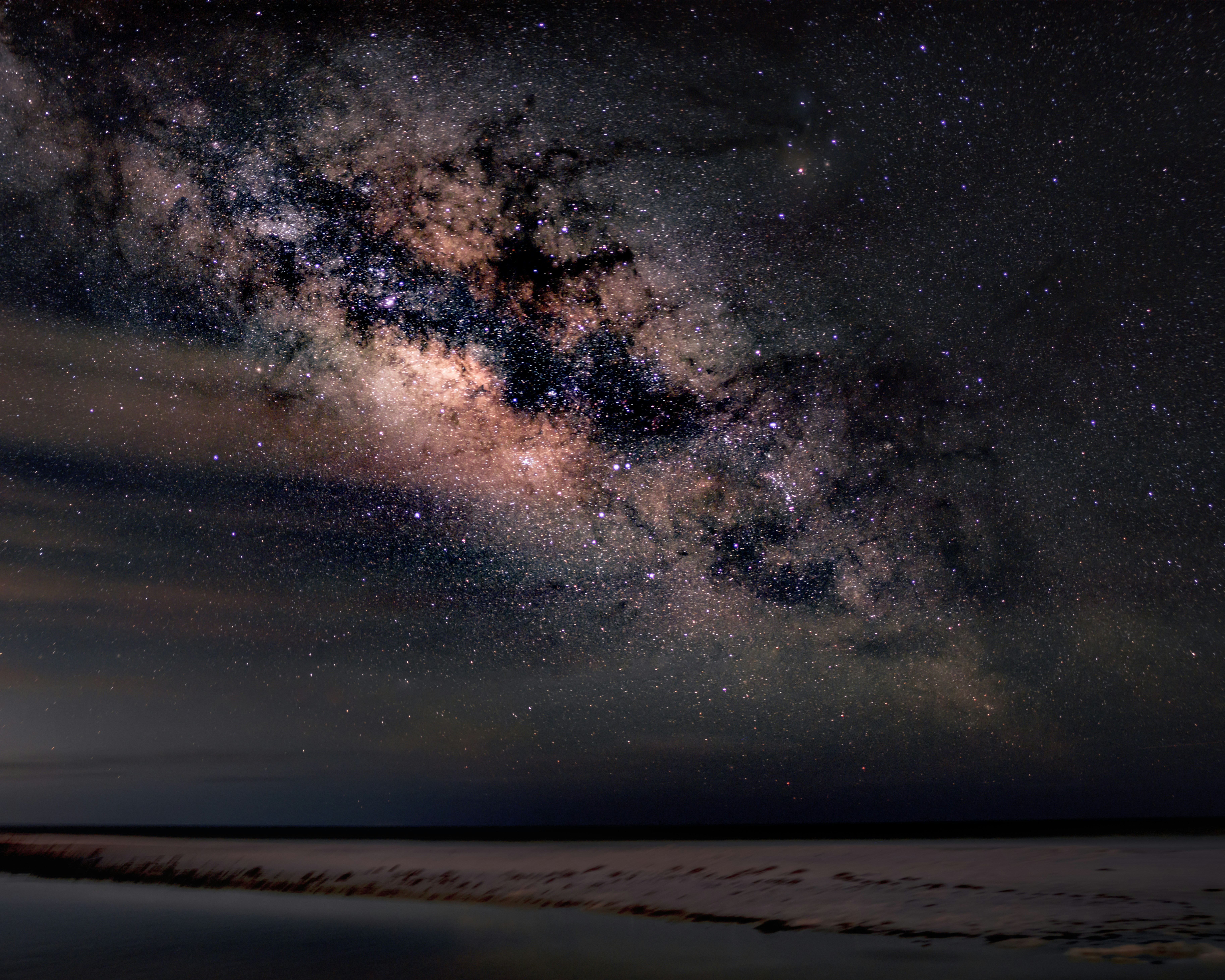 The Milky Way stretches across a clear night sky above a peaceful coastal shoreline.