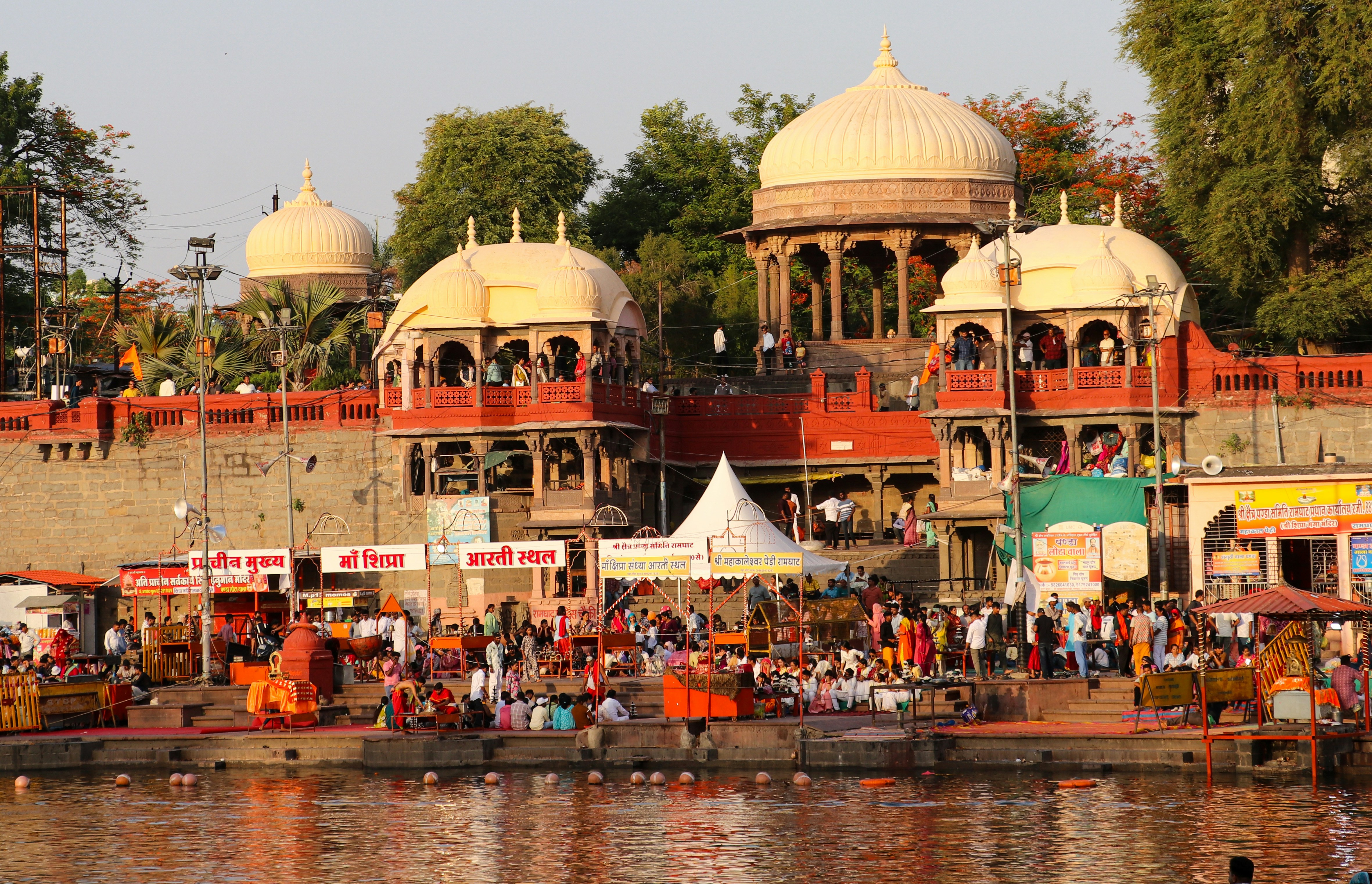 Hindu temple complex by the riverbank during a lively daytime gathering