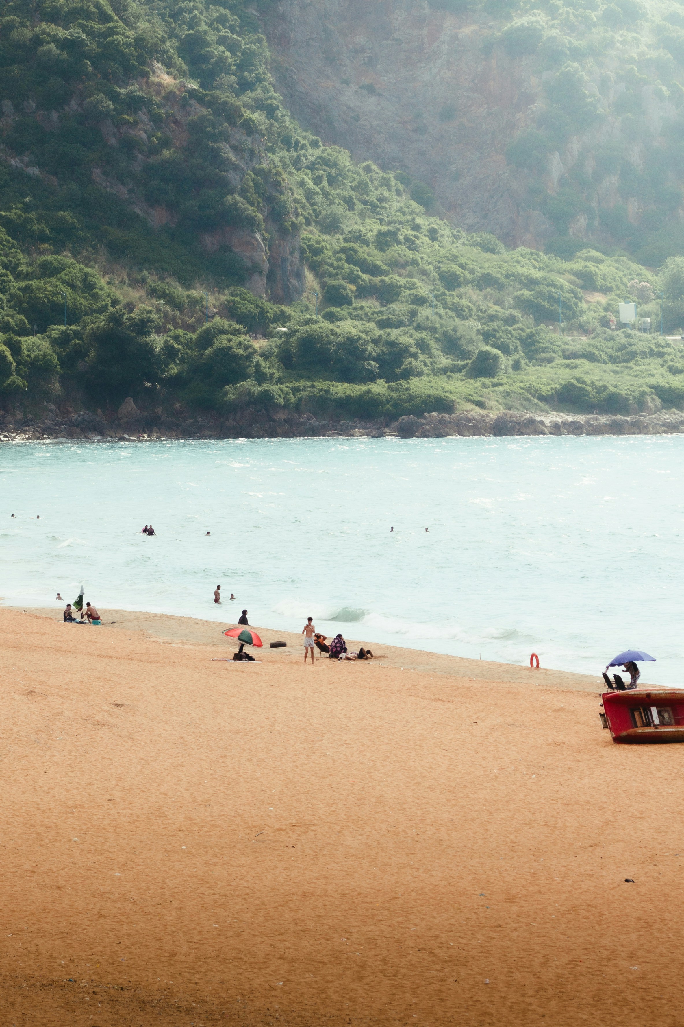 Coastal Beachgoers Beneath Verdant Cliffs on Sunlit Shore
