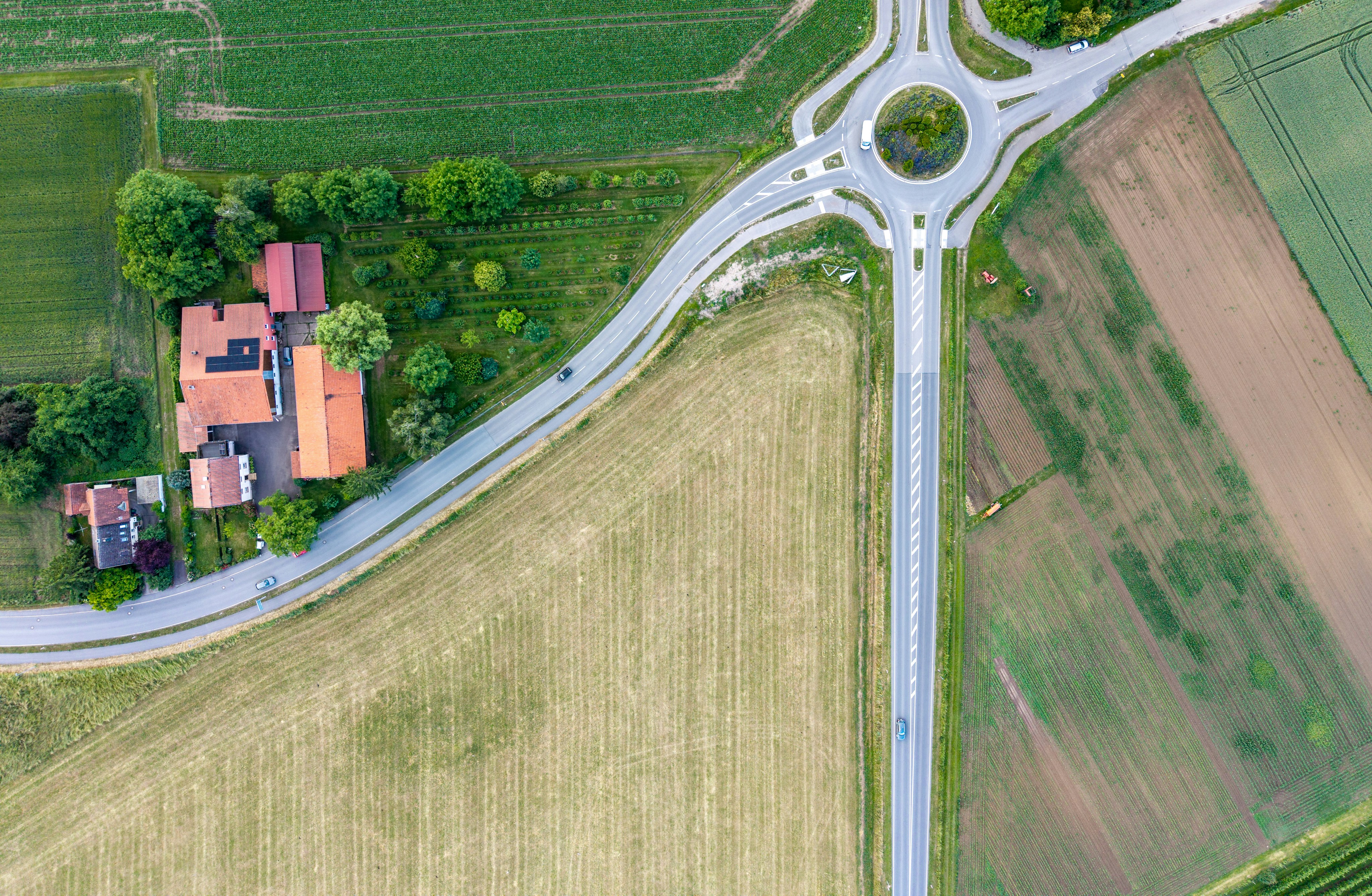 Overhead view of a rural roundabout, roads, fields, and buildings.
