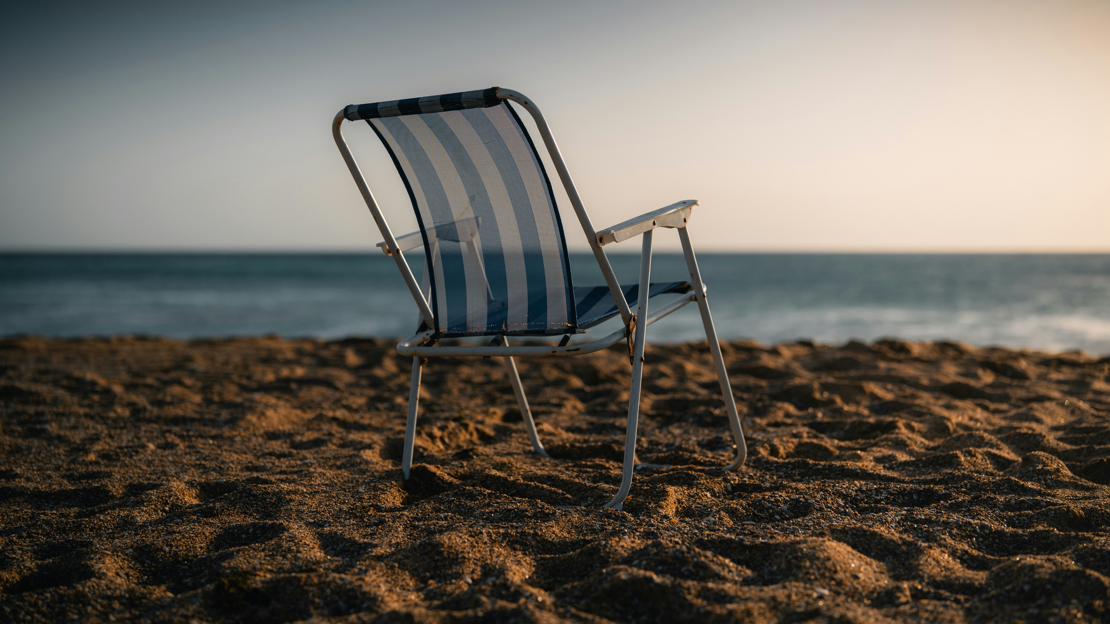 A striped beach chair on sandy beach overlooking the ocean.