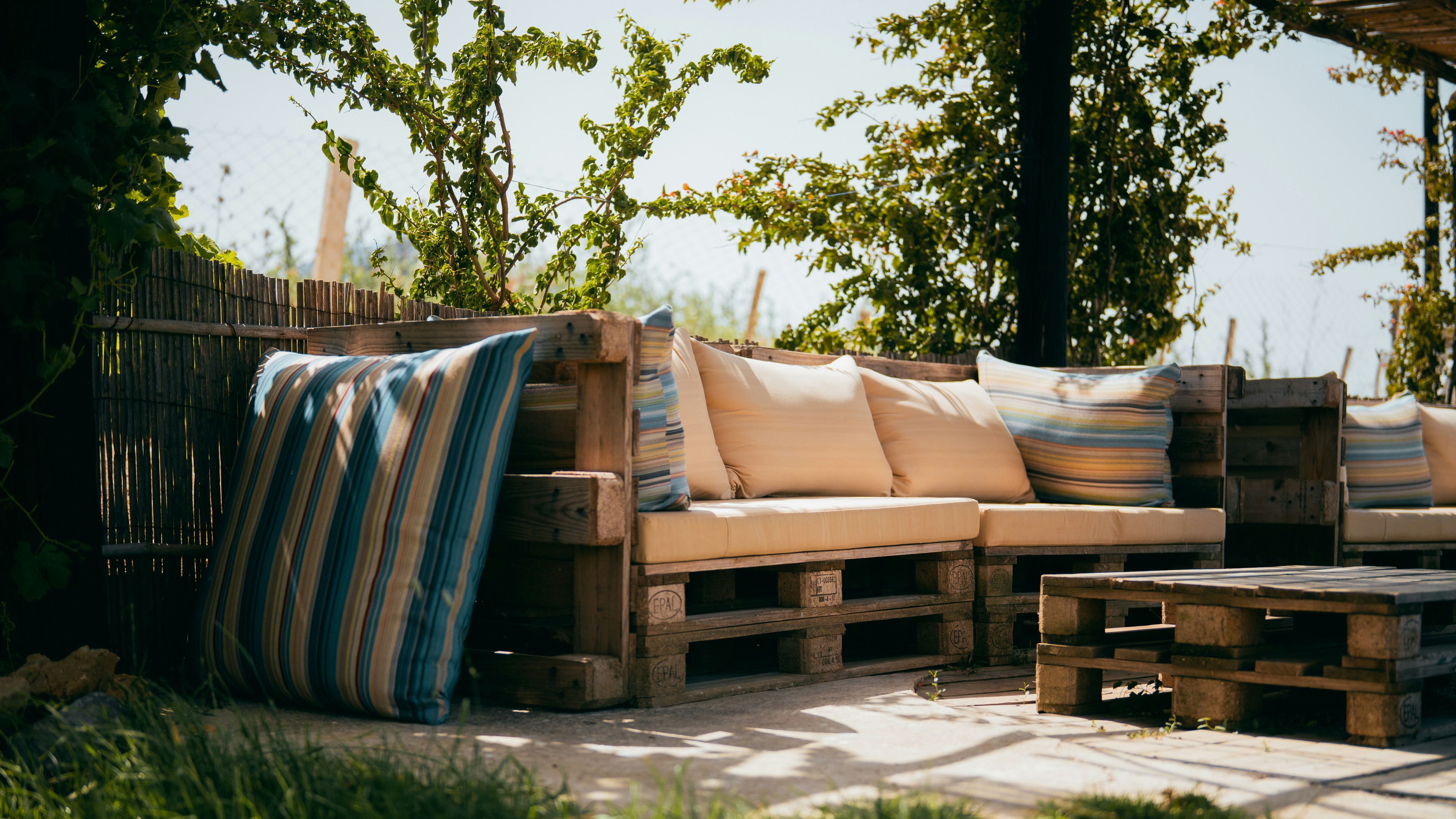 Sunlit Outdoor Lounge with Striped Cushions under a Shaded Pergola