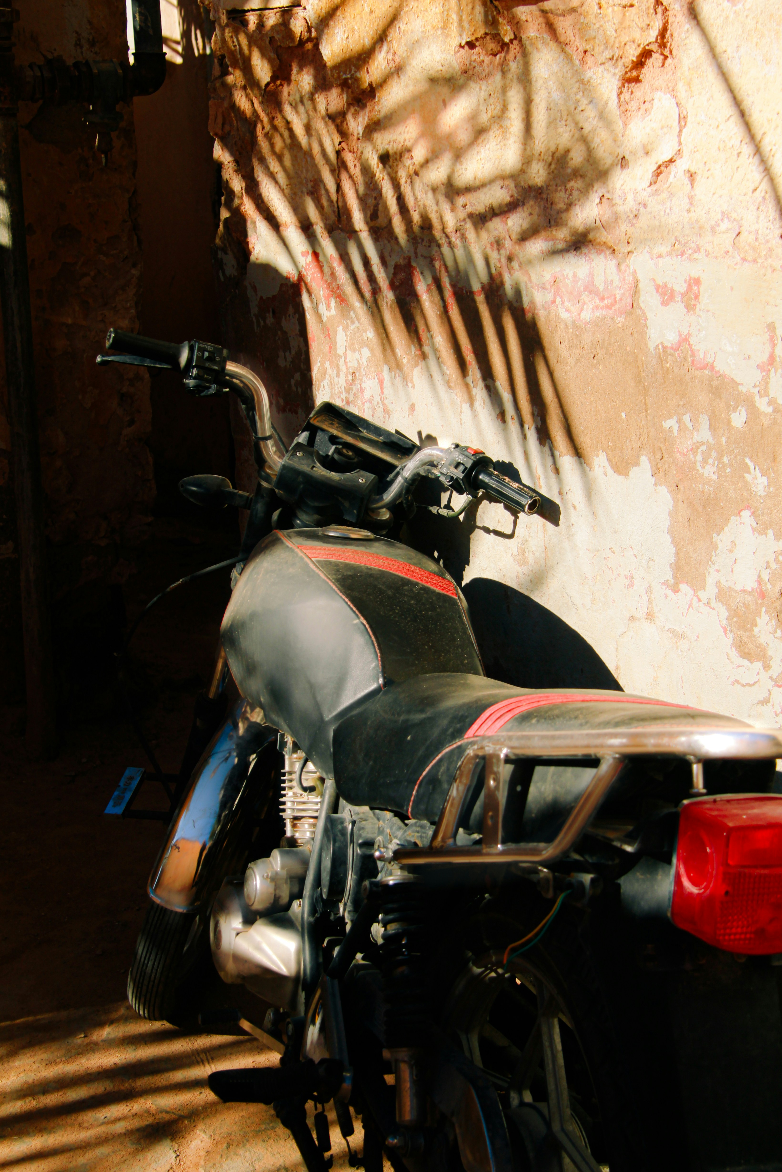 Trail of Rust and Sunlight: A Motorcycle in a Worn Courtyard