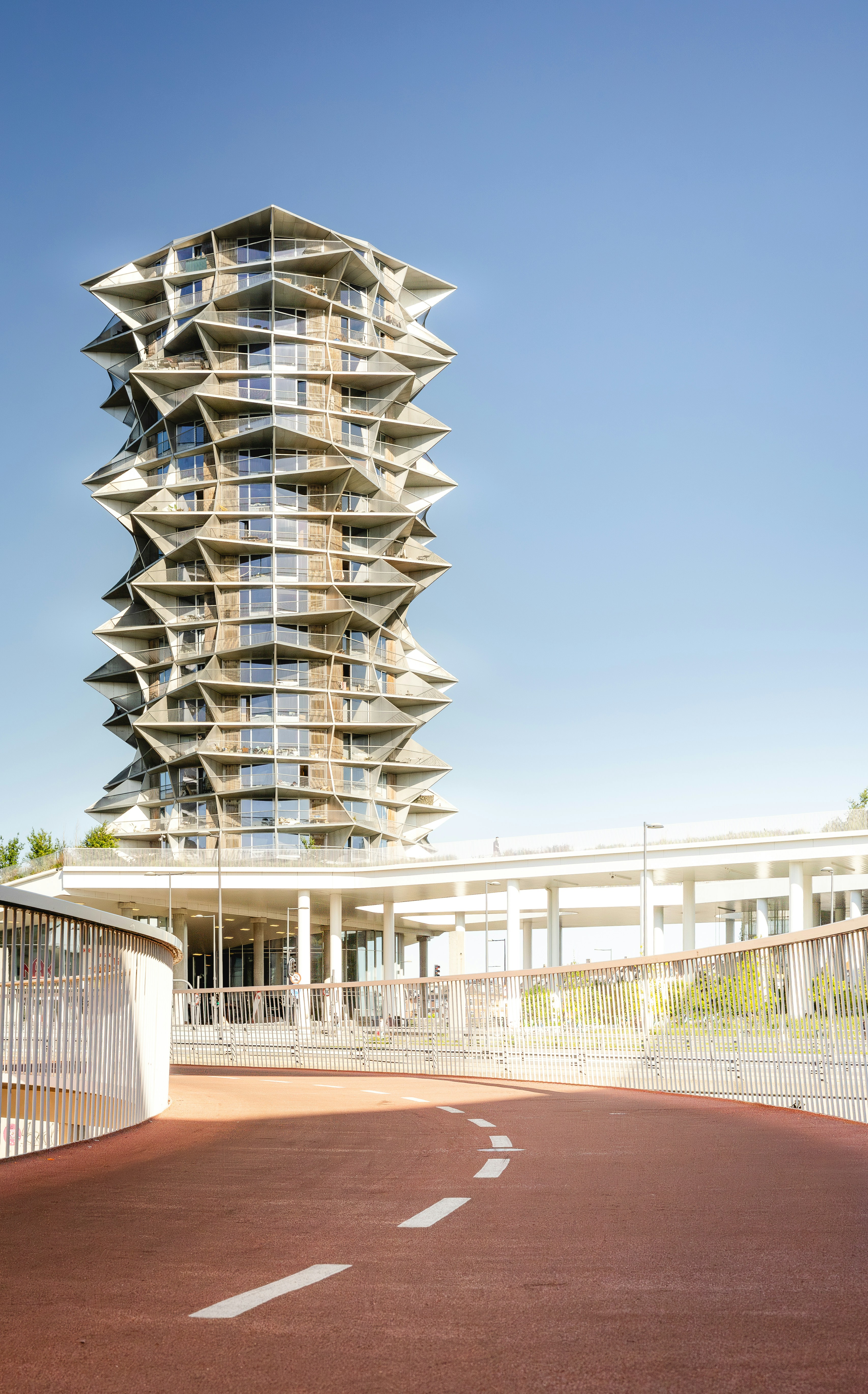 The Kaktus tower with rotating leaf-shaped floor plates rises organically against a clear blue sky, with a sweeping red cycle path in the foreground.