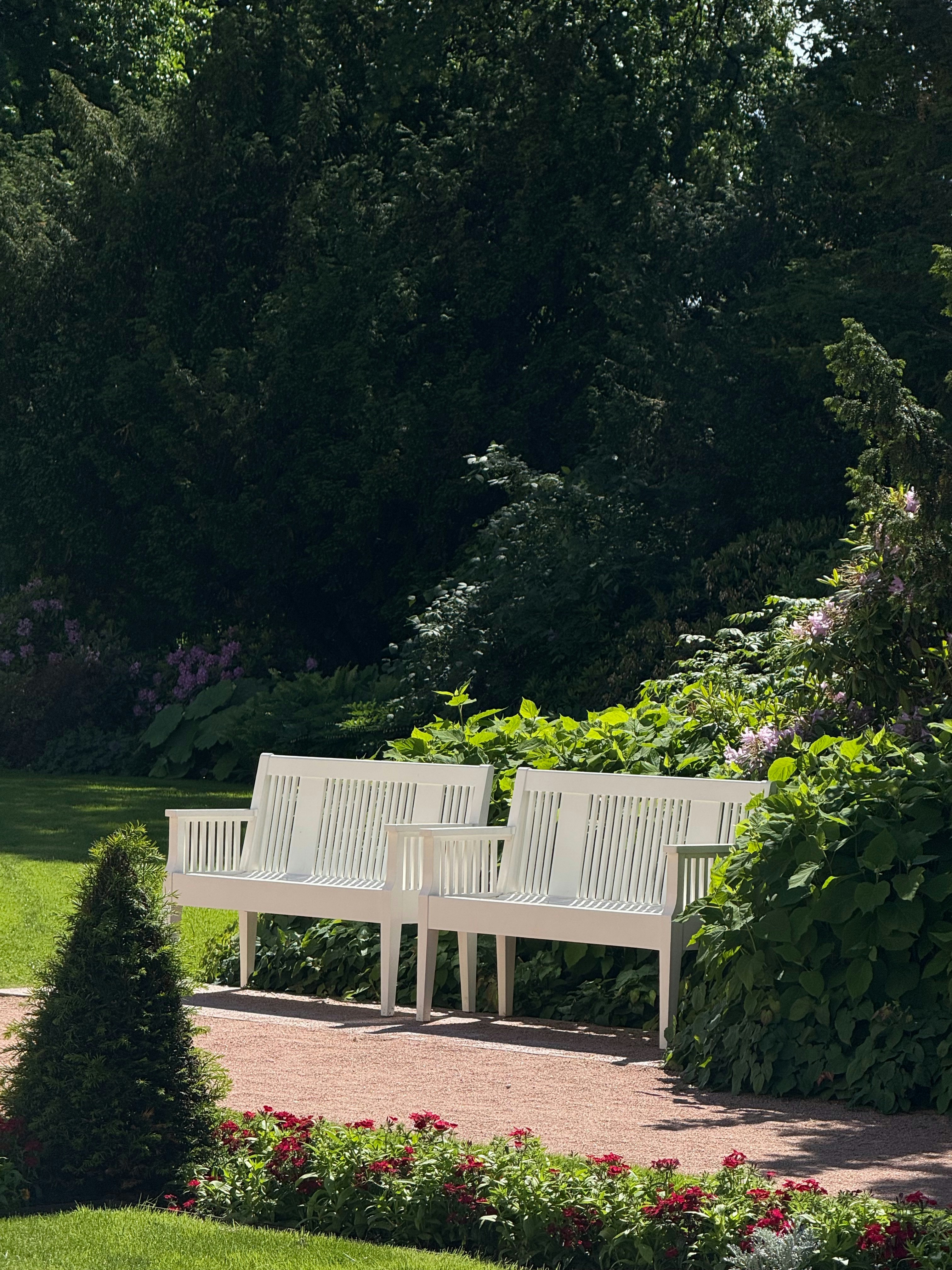 White Garden Benches Resting at the Edge of Blooming Borders