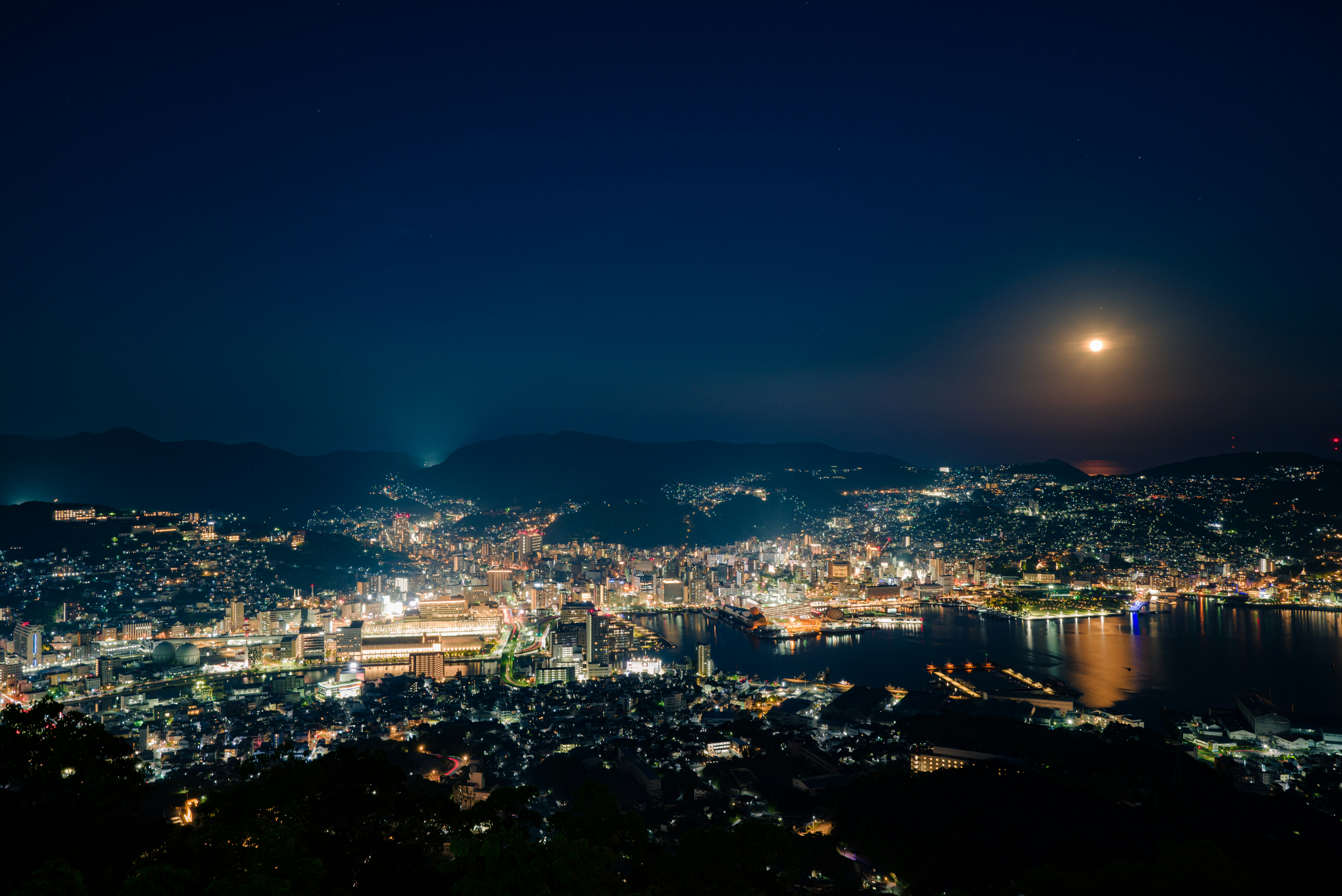 A vibrant city skyline at night with a full moon.