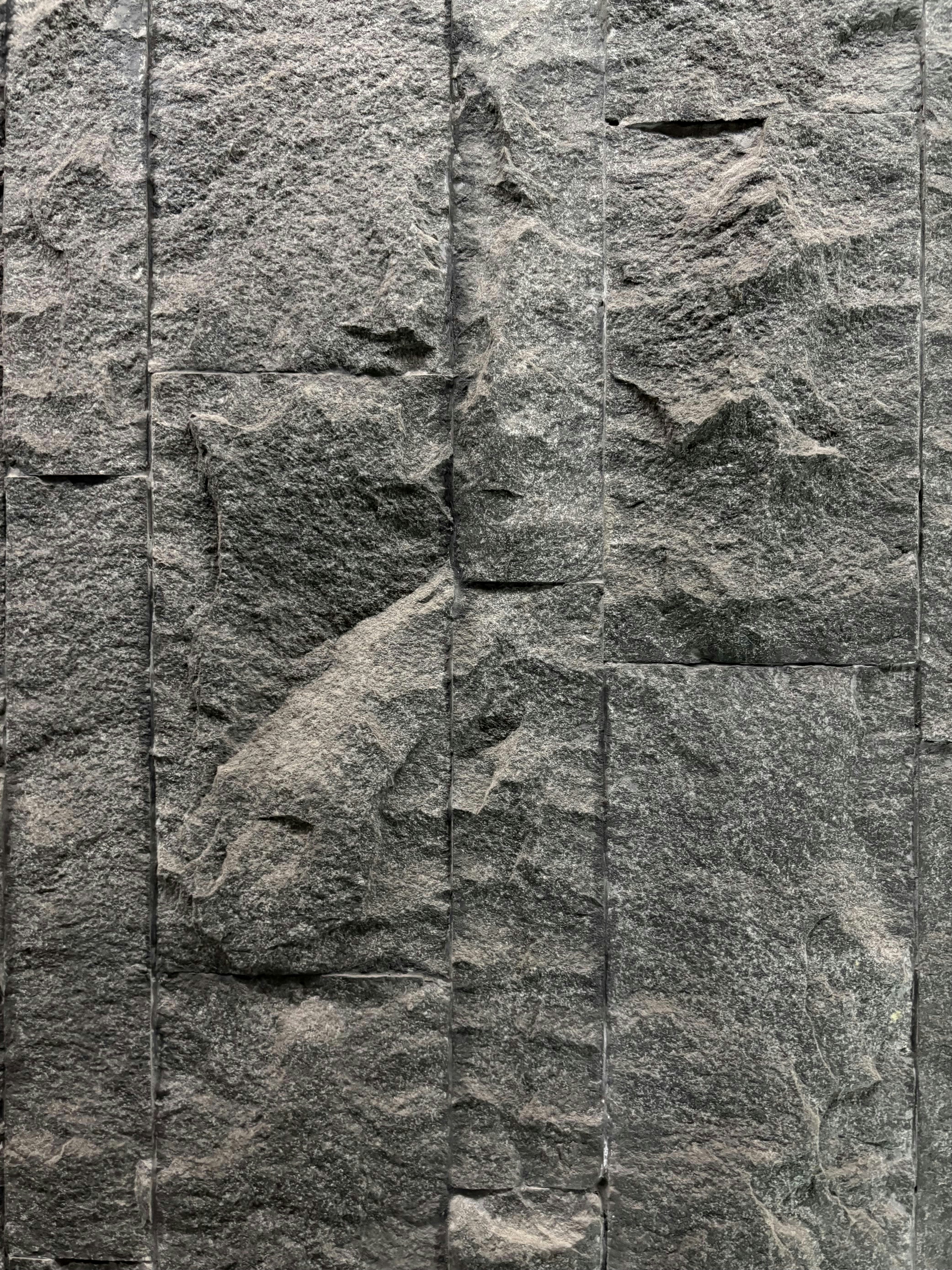 Textured dark grey stone wall with vertical tiles.