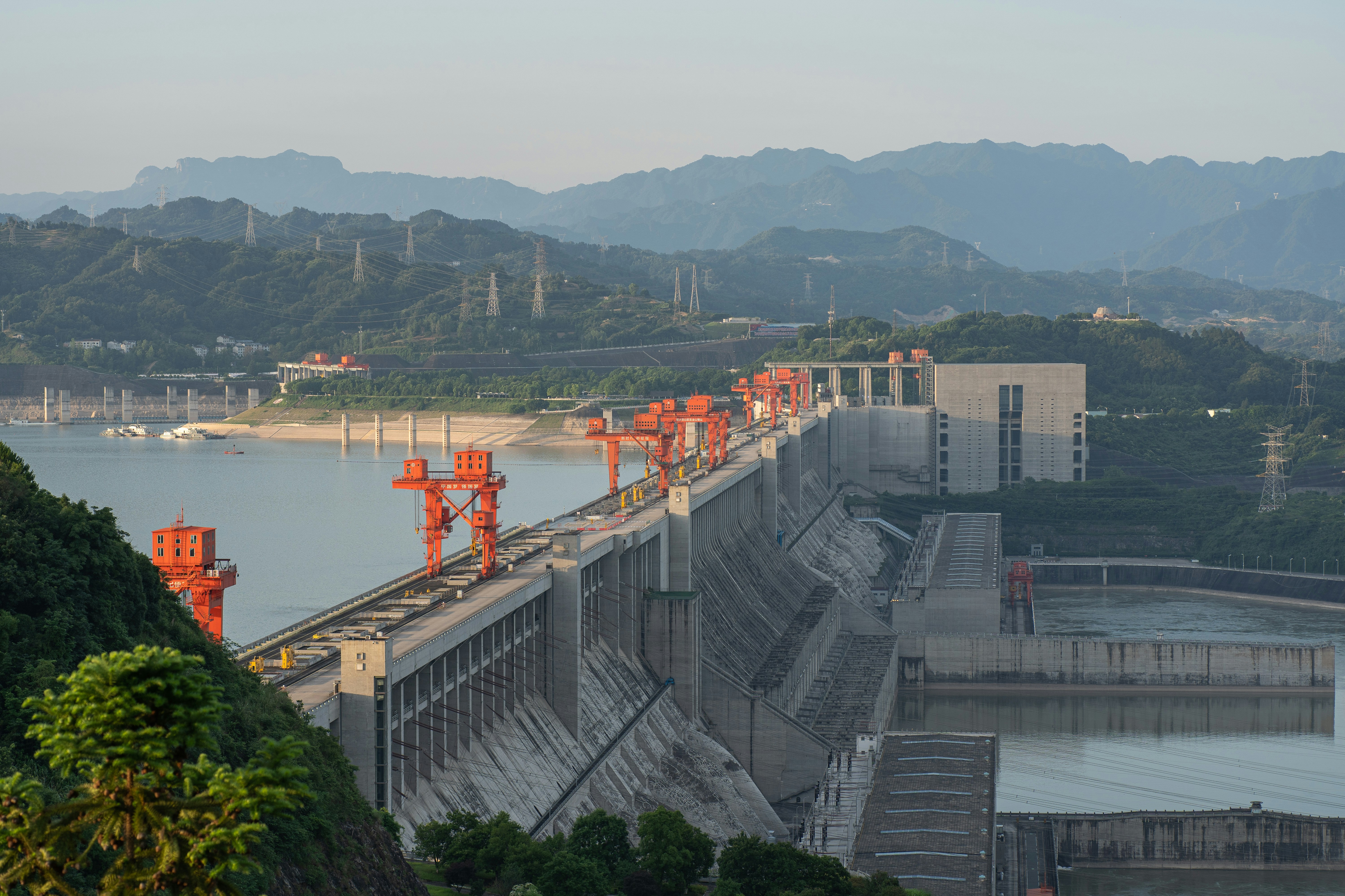 Massive hydroelectric dam with red structures against a mountain backdrop.