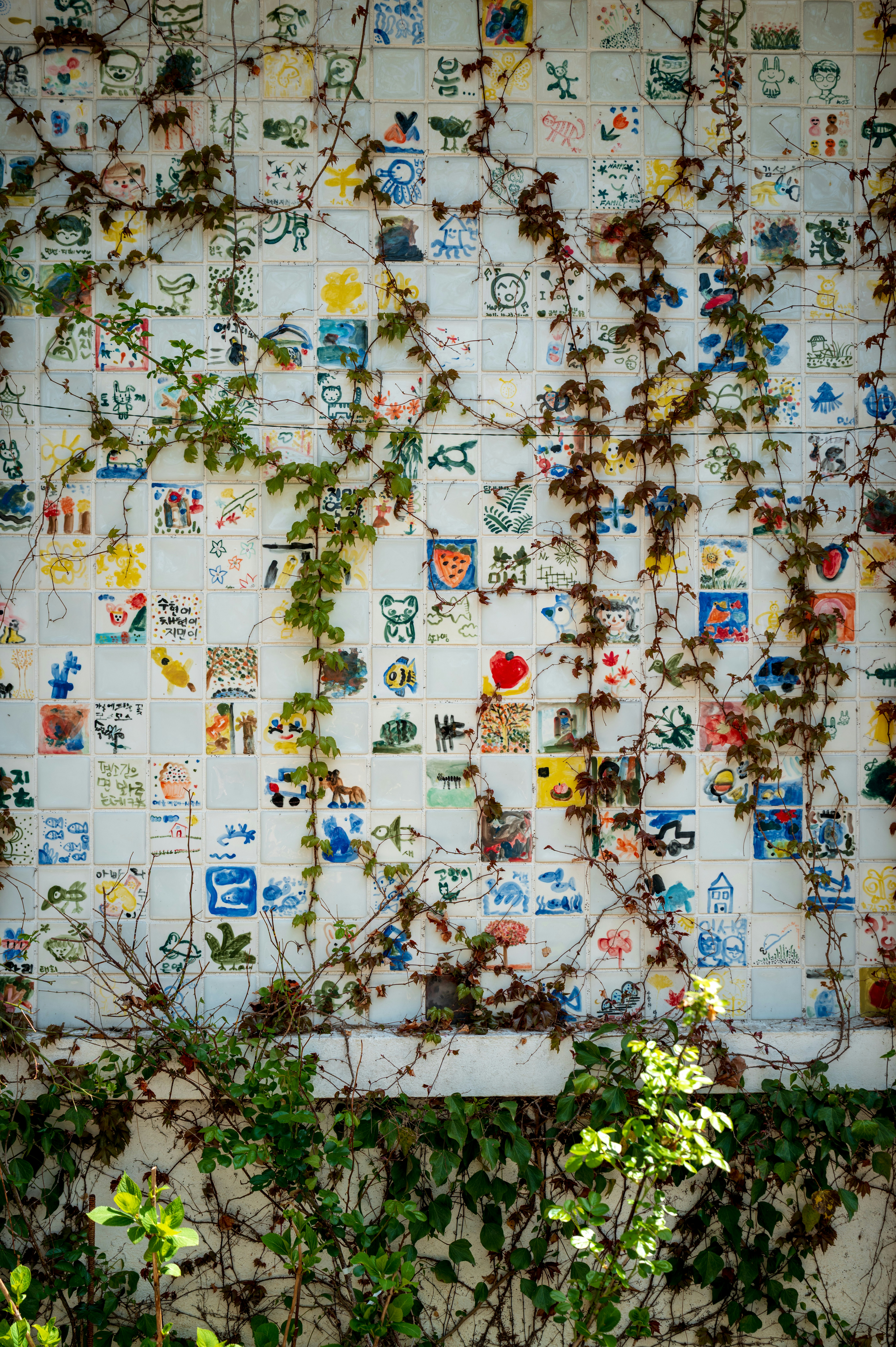 A tiled wall covered with colorful drawings and green vines.