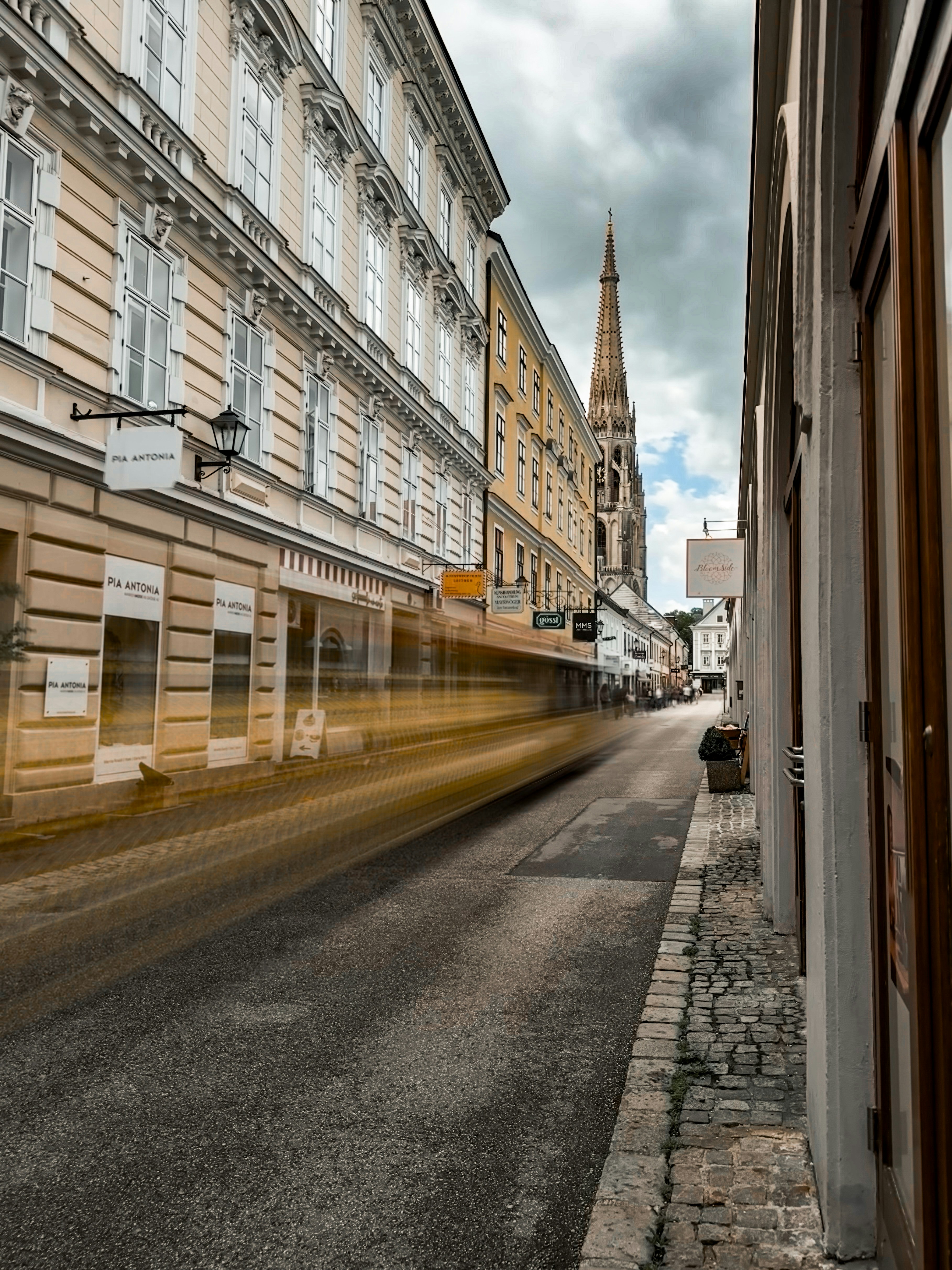 Chapel spire meets streetlight glow: a passing tram blurs through a cobblestone lane