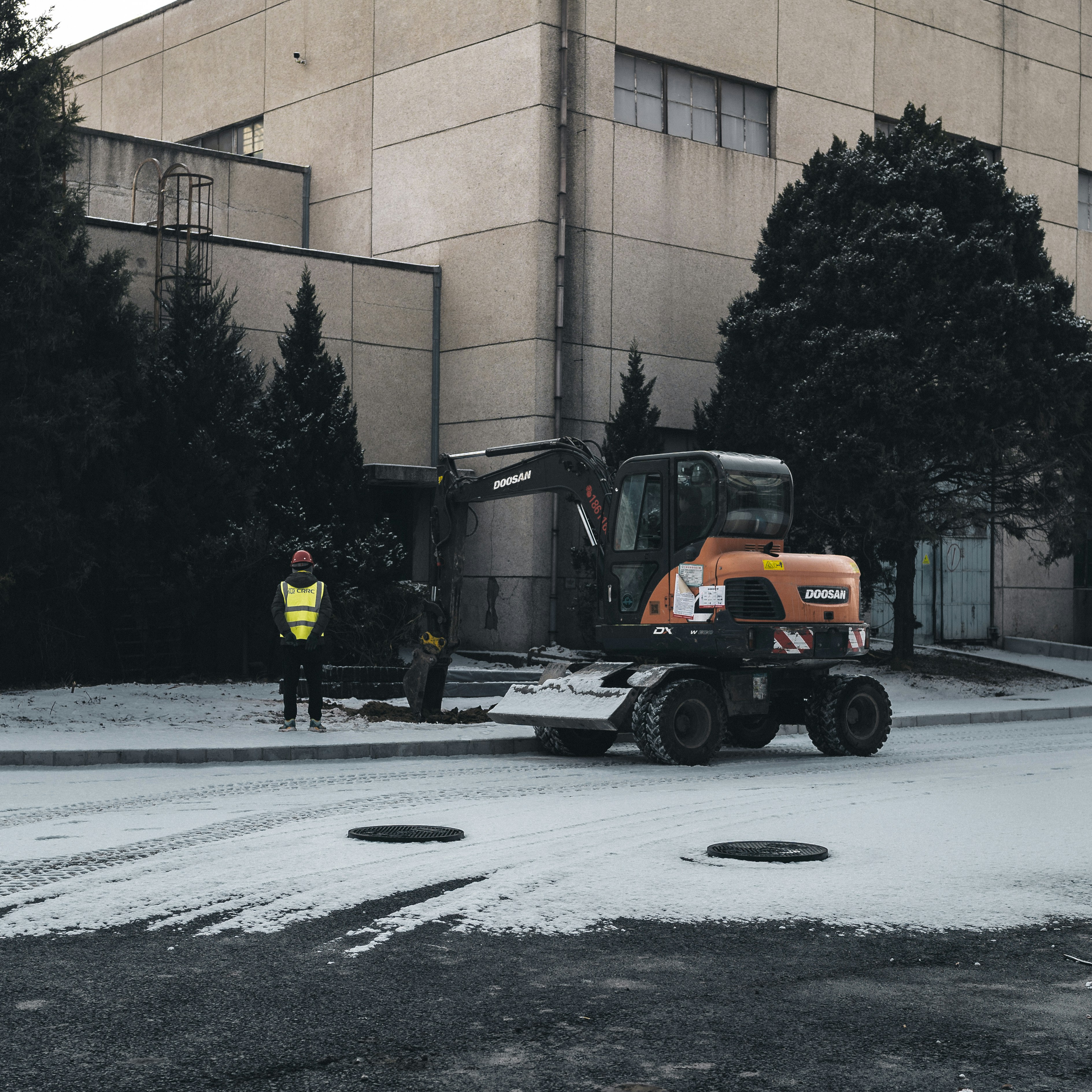 Construction worker and excavator on a snowy winter road.
