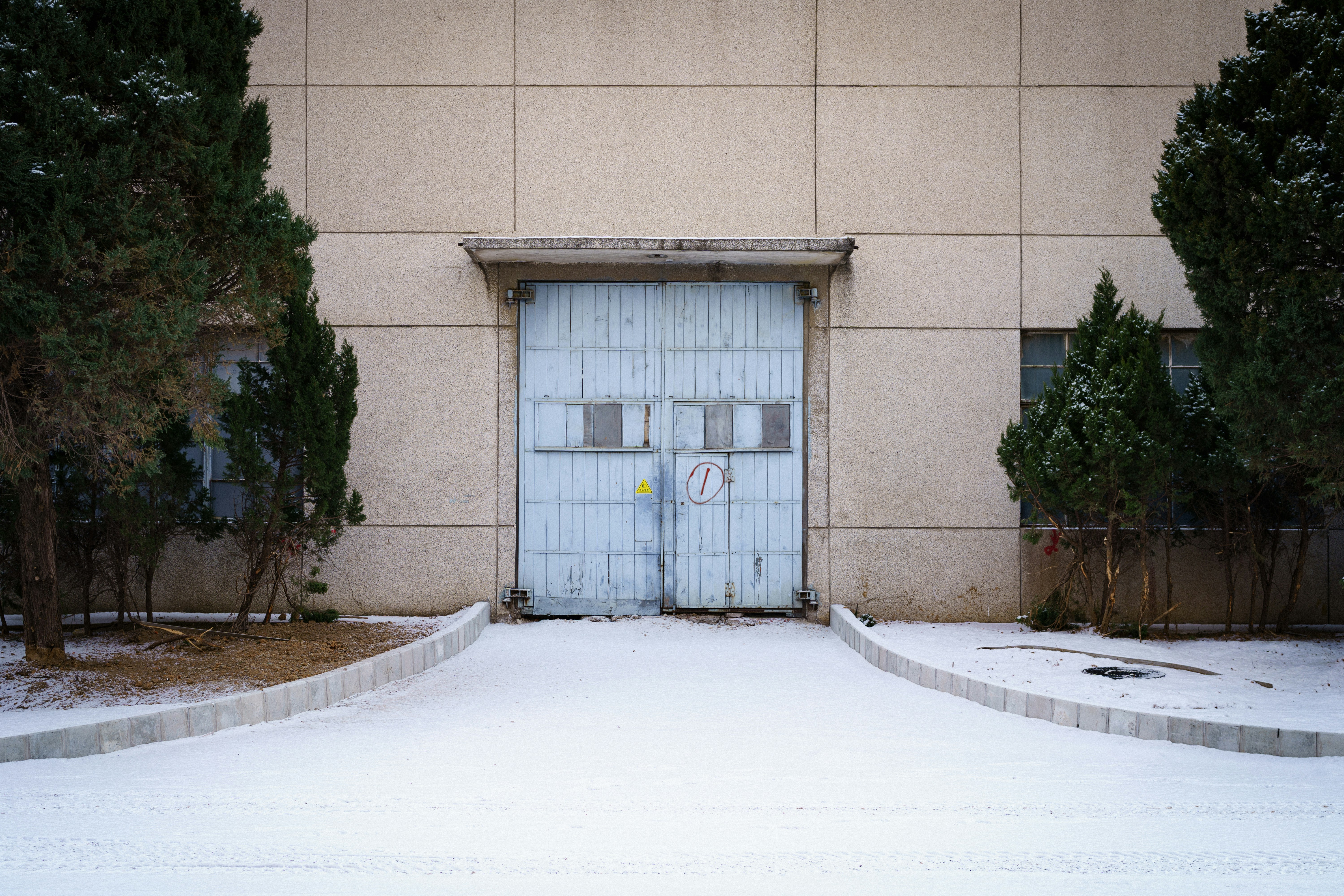 Faded blue garage door on a building, surrounded by snow.