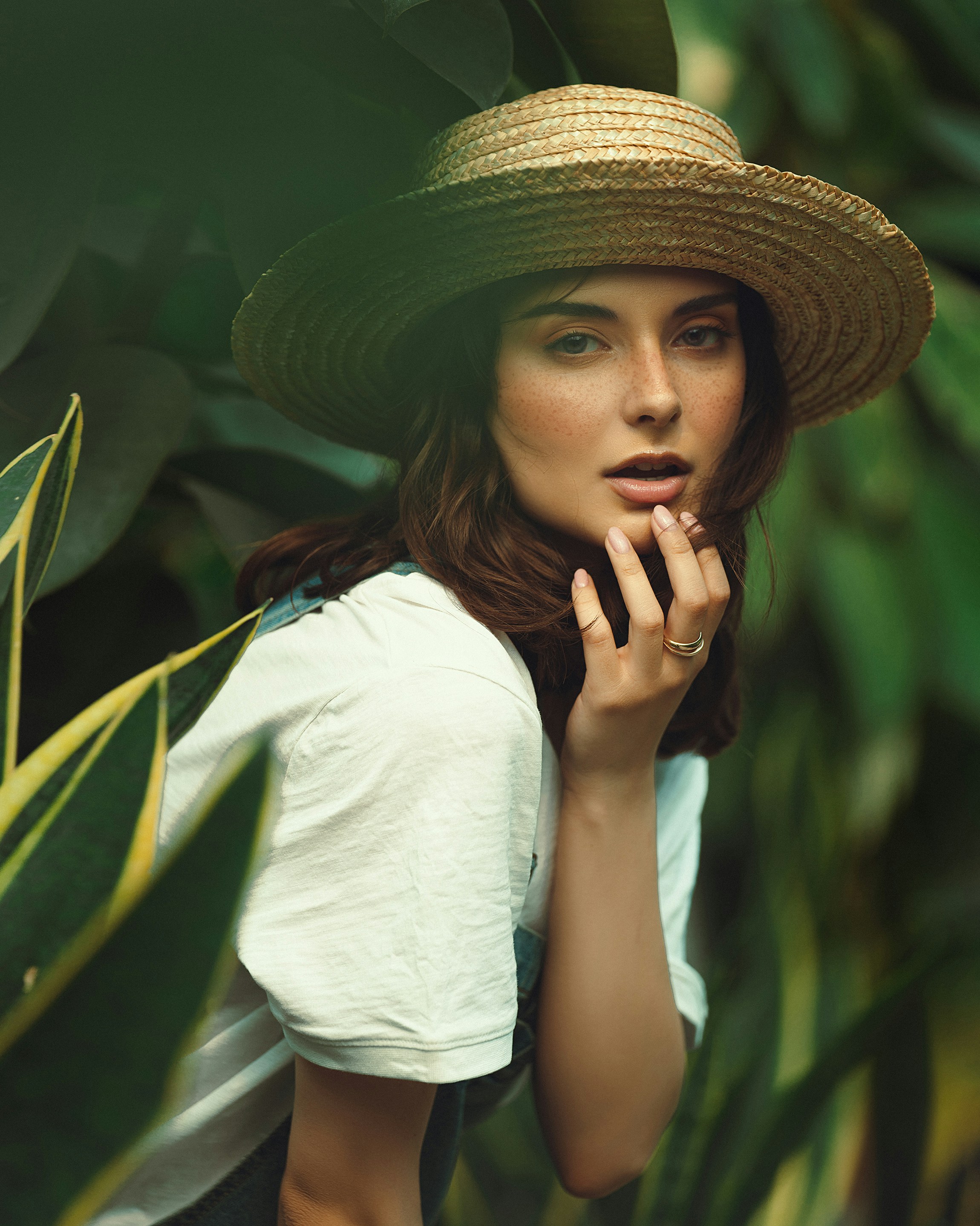 Woman in straw hat looking out from green tropical foliage.