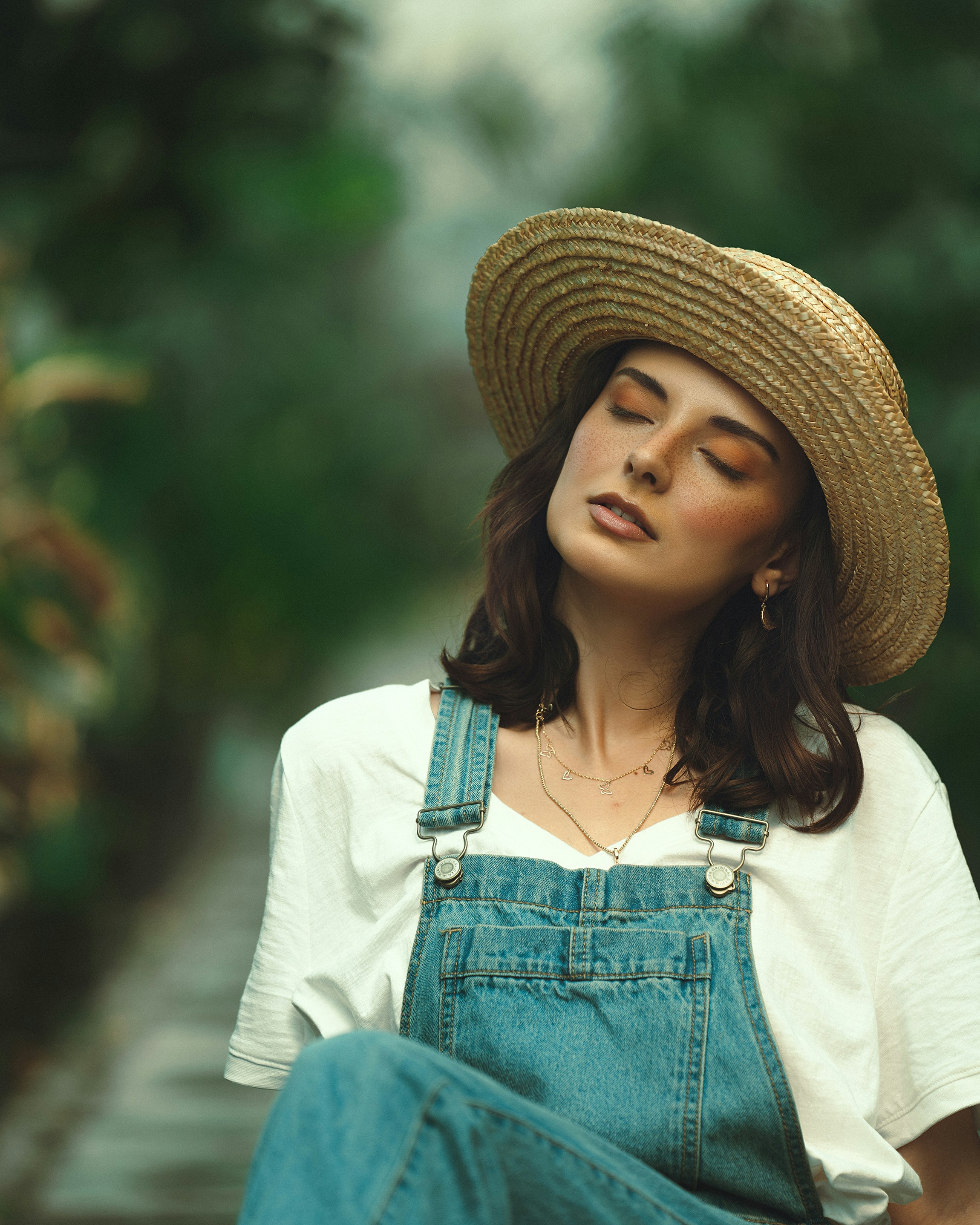 Woman in straw hat and overalls relaxing outdoors.