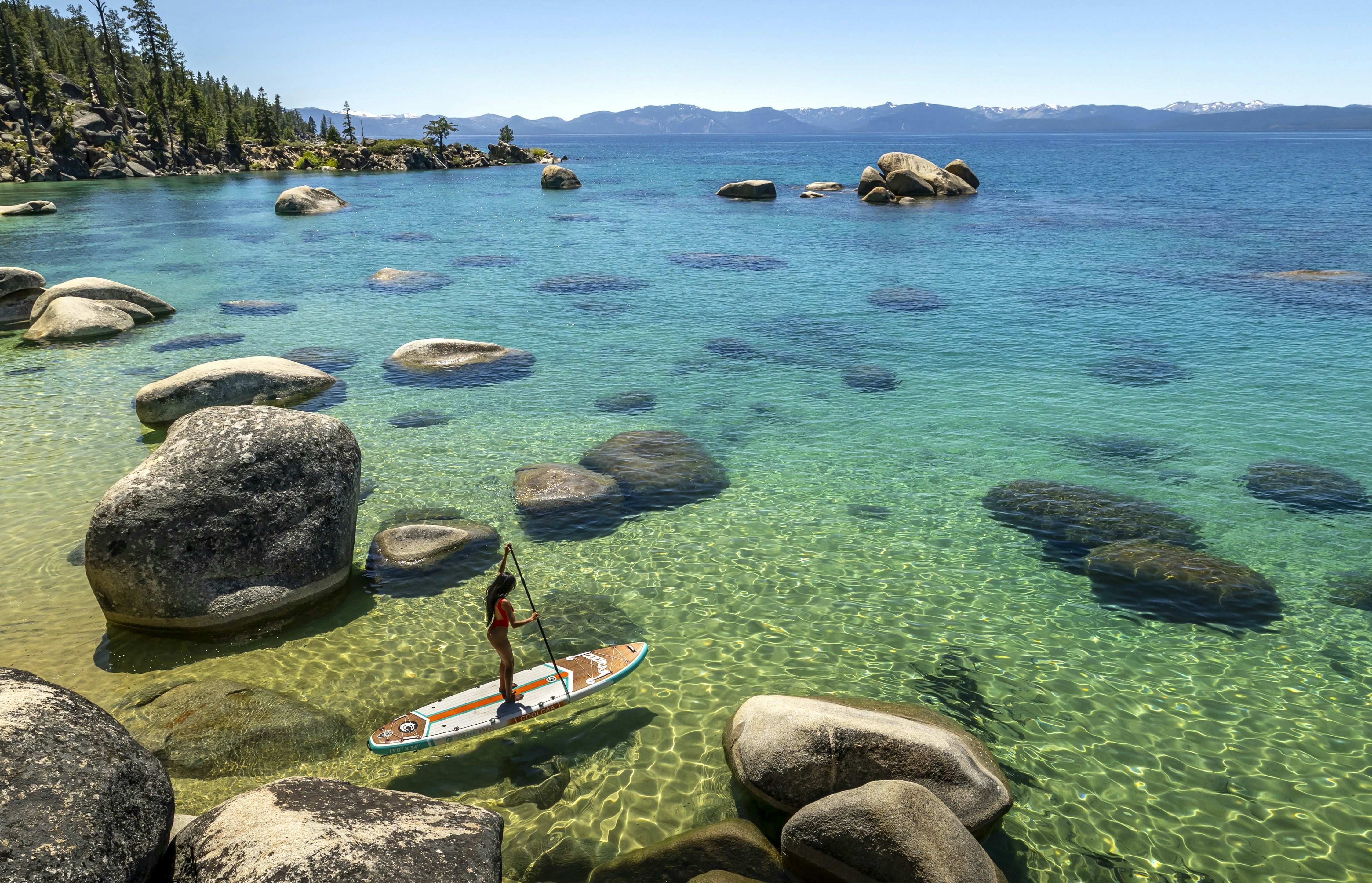 Woman paddleboarding in clear blue lake surrounded by rocks.