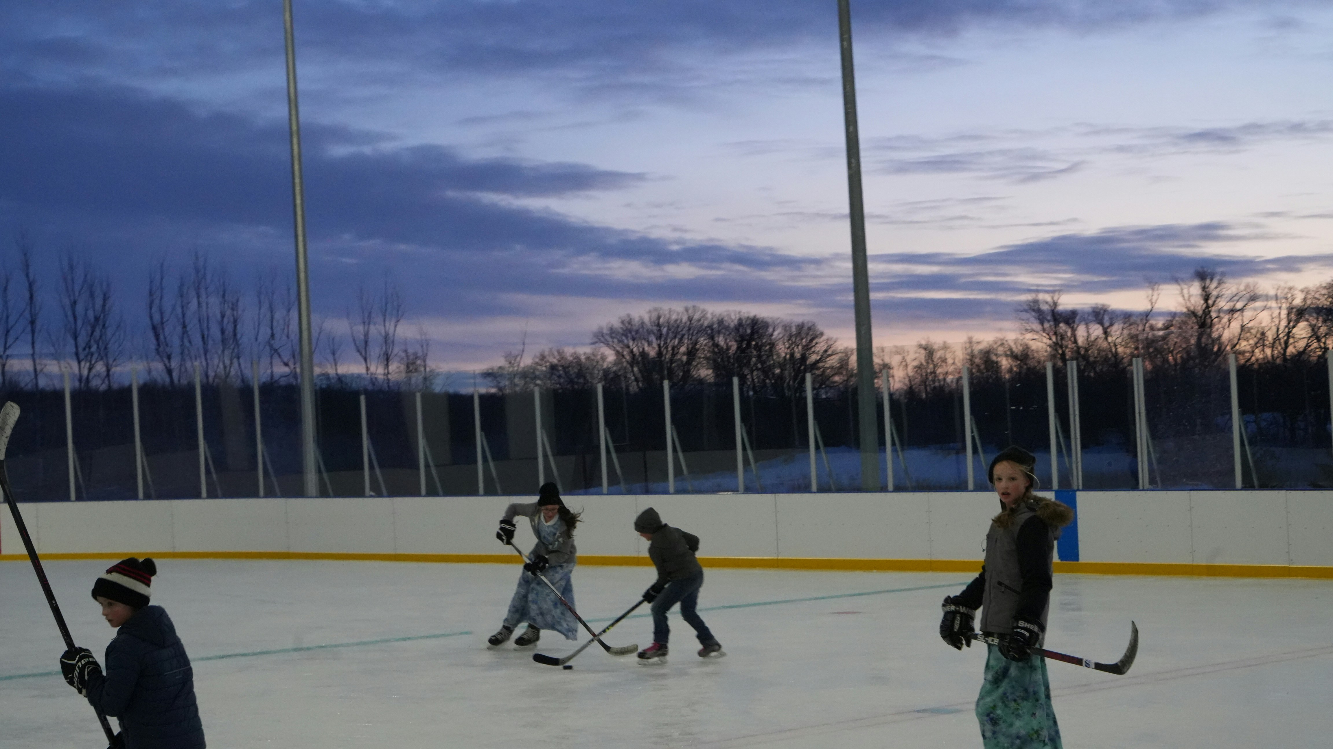Hutterite children playing hockey at sunset in traditional dress. Manitoba, Canada.