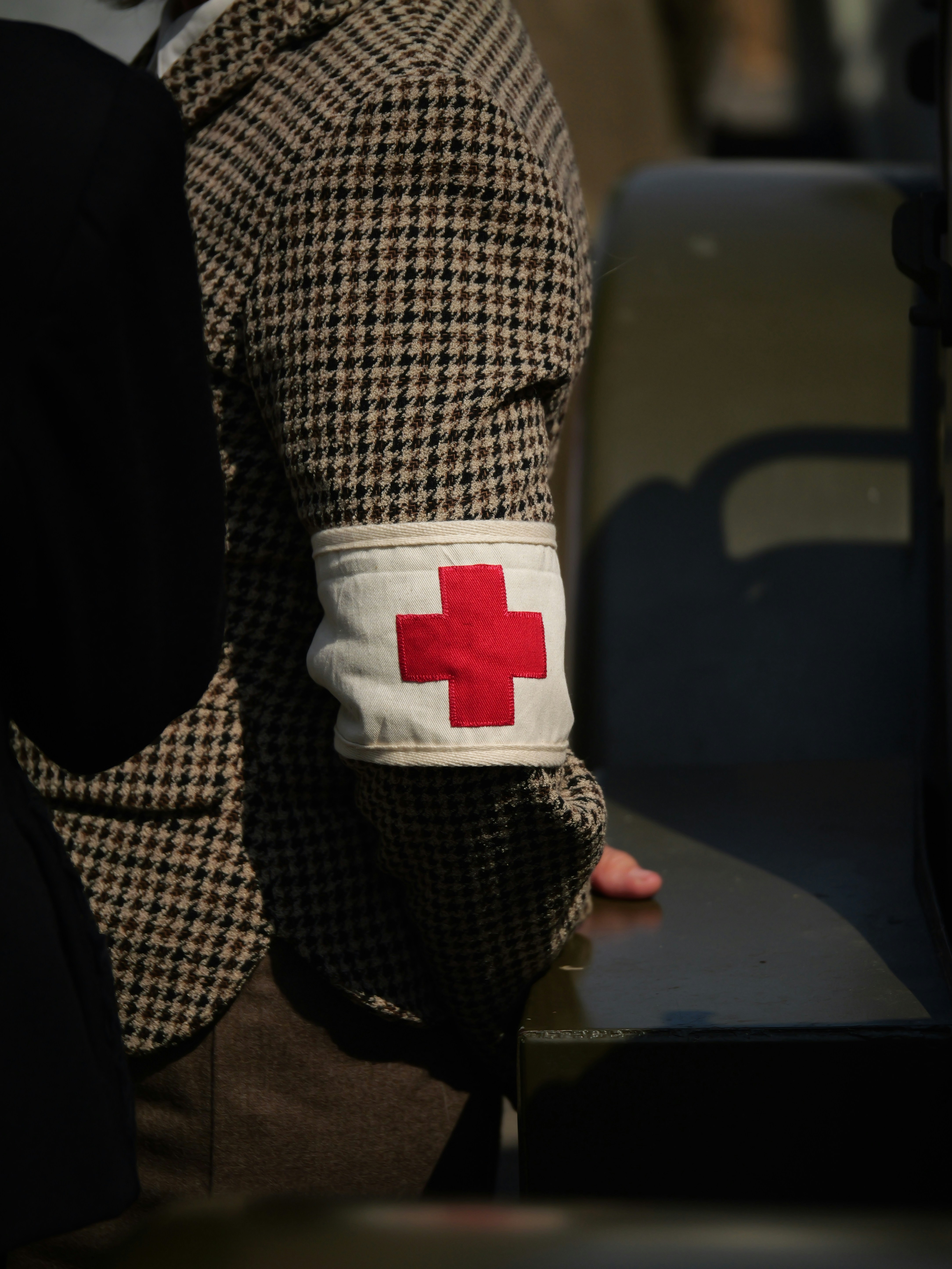 Red cross armband on a person's houndstooth jacket.