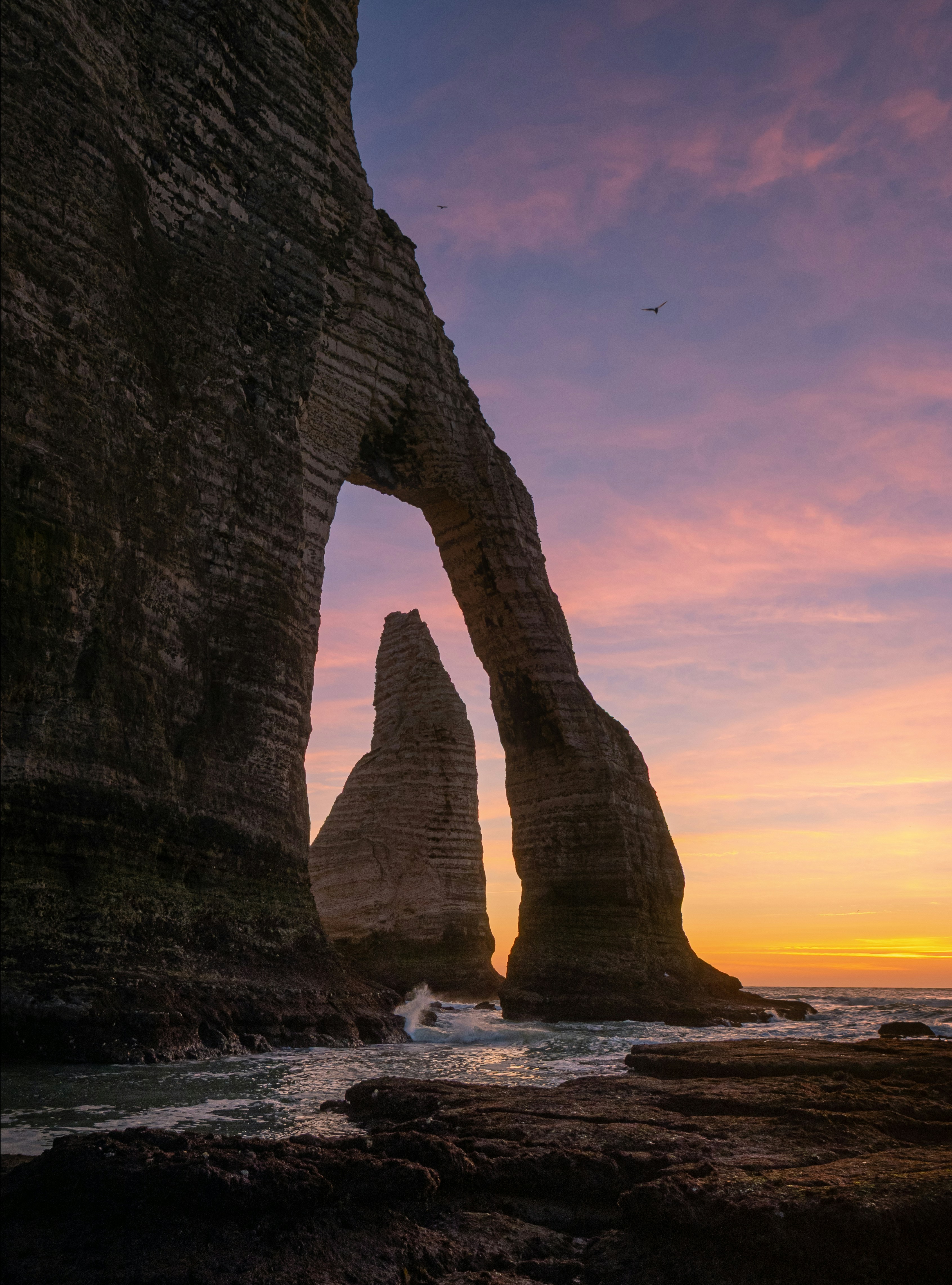 Dramatic rock arches and sea stacks at colorful sunset.