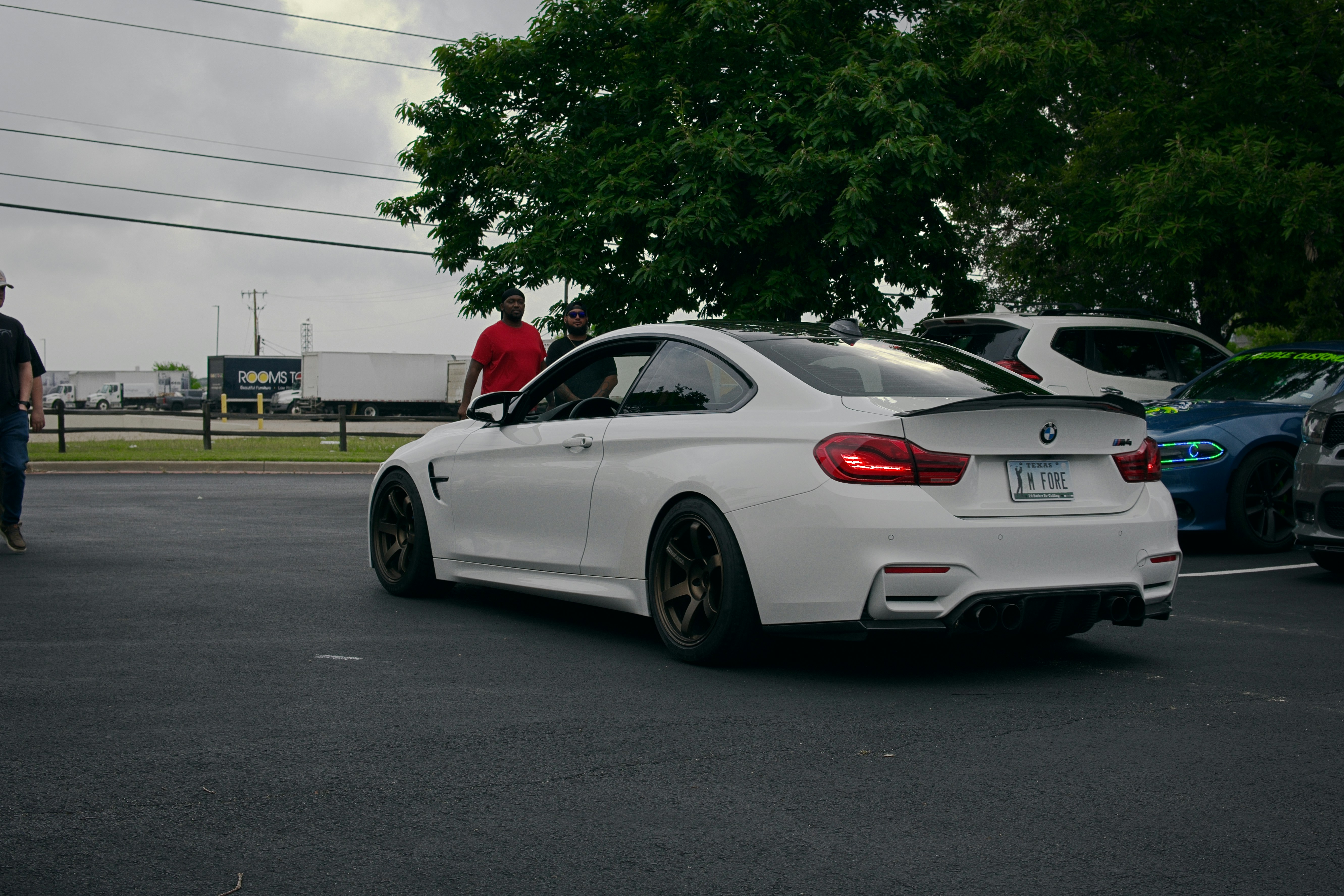 White BMW M4 in a parking lot, tail lights glowing under overcast sky