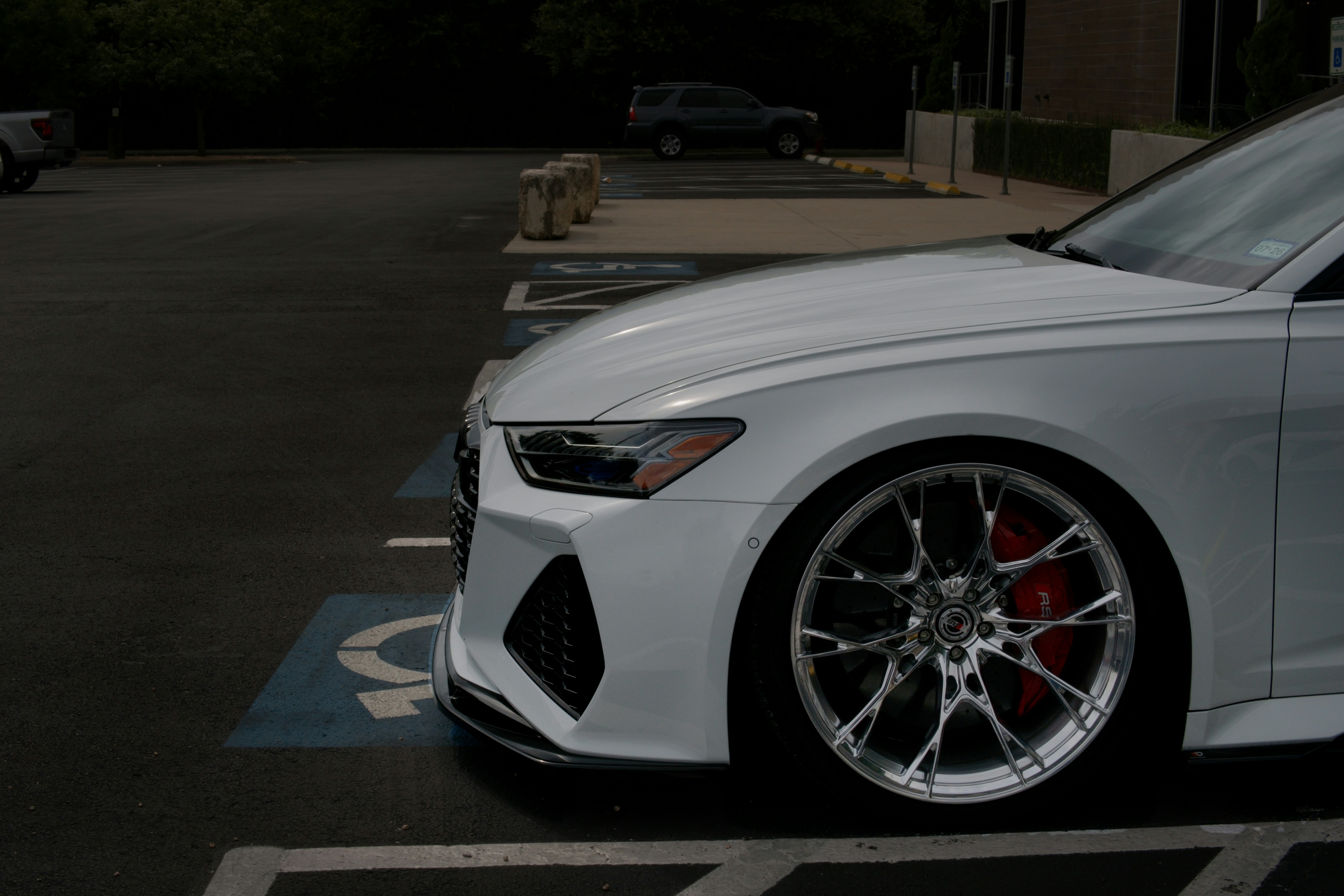Low-angle reveal: the aggressive front wheel and vented bumper of a white sports sedan